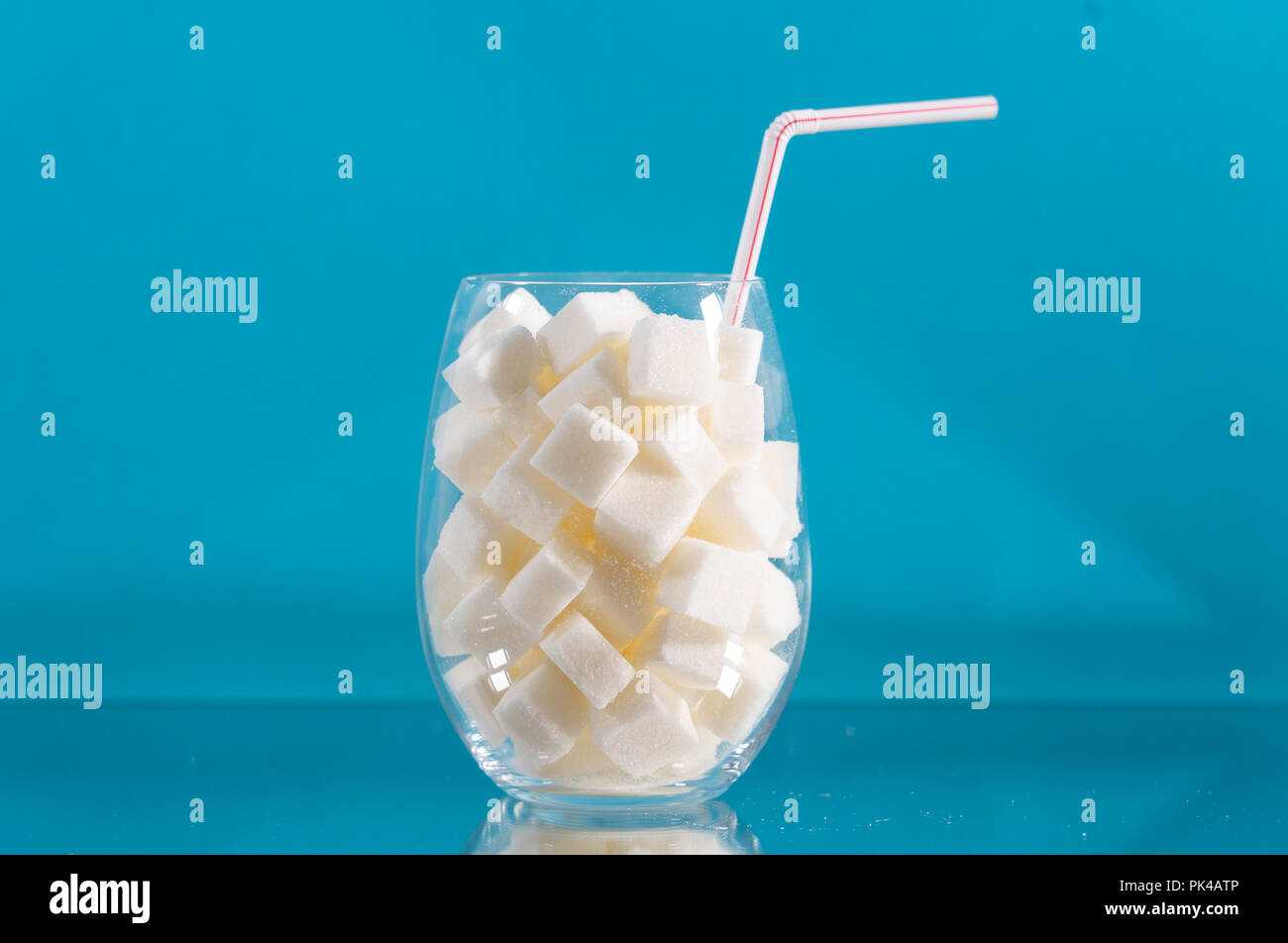 Glass with red stripes straw filled with sugar cubes on blue background ...