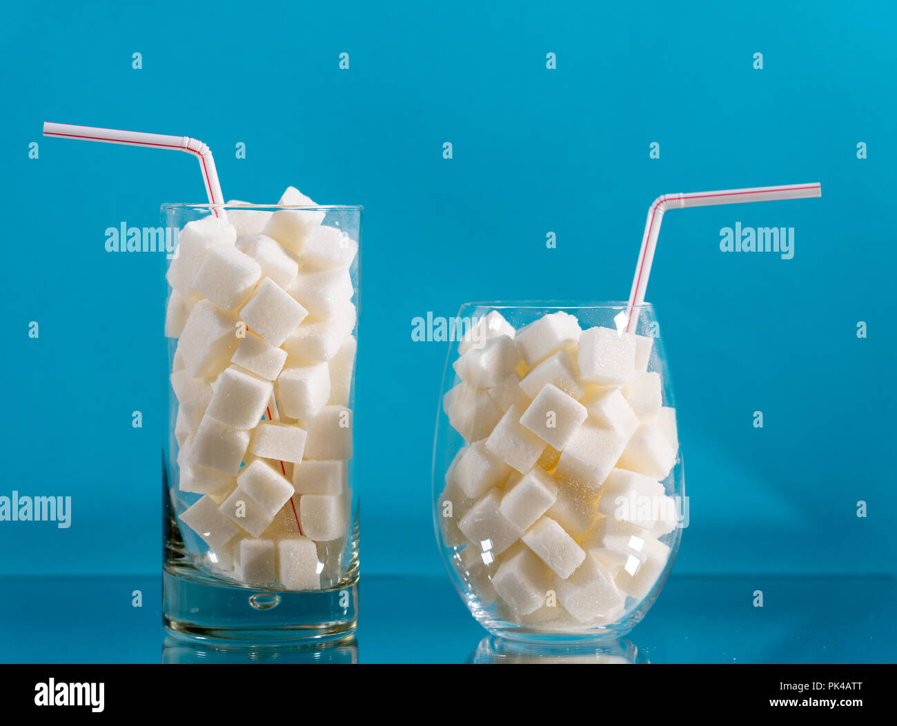 Glass with red stripes straw filled with sugar cubes on blue background ...