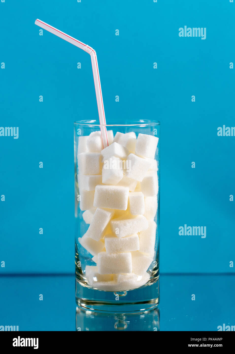 Glass with red stripes straw filled with sugar cubes on blue background ...