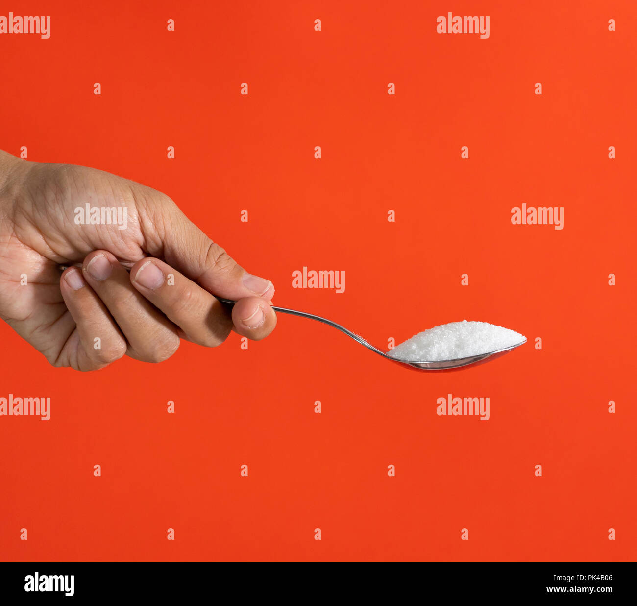 Woman hand holding and offering a spoon full of sugar isolated on a red ...