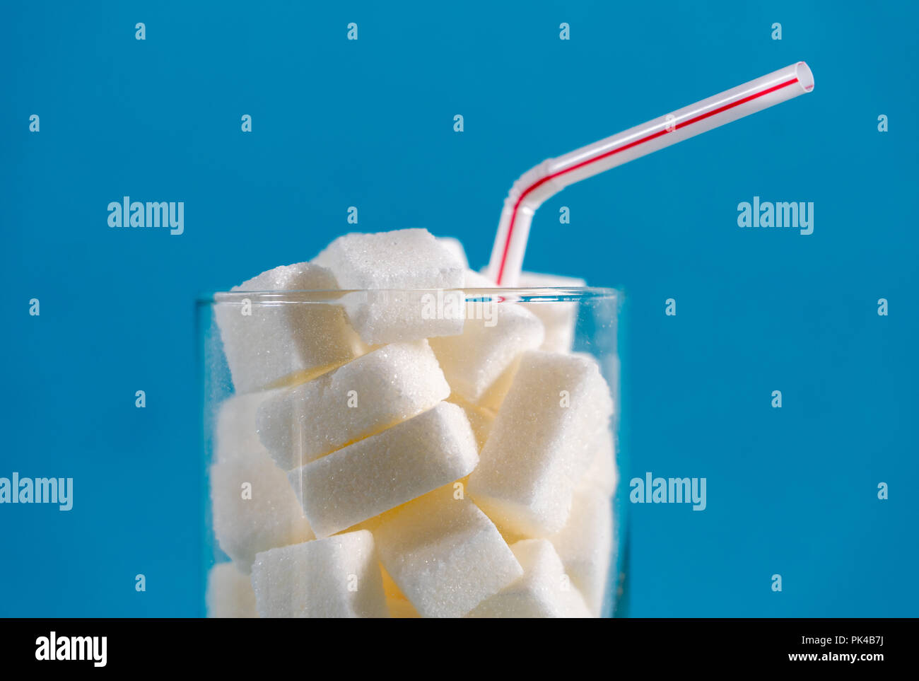 Glass with red stripes straw filled with sugar cubes on blue background ...