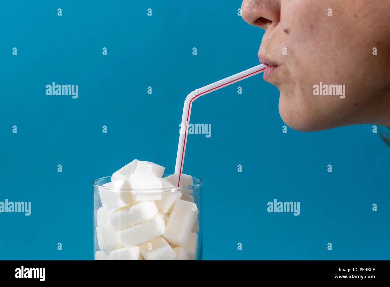 Profile of a young woman drinking with a red stripes straw from a glass ...