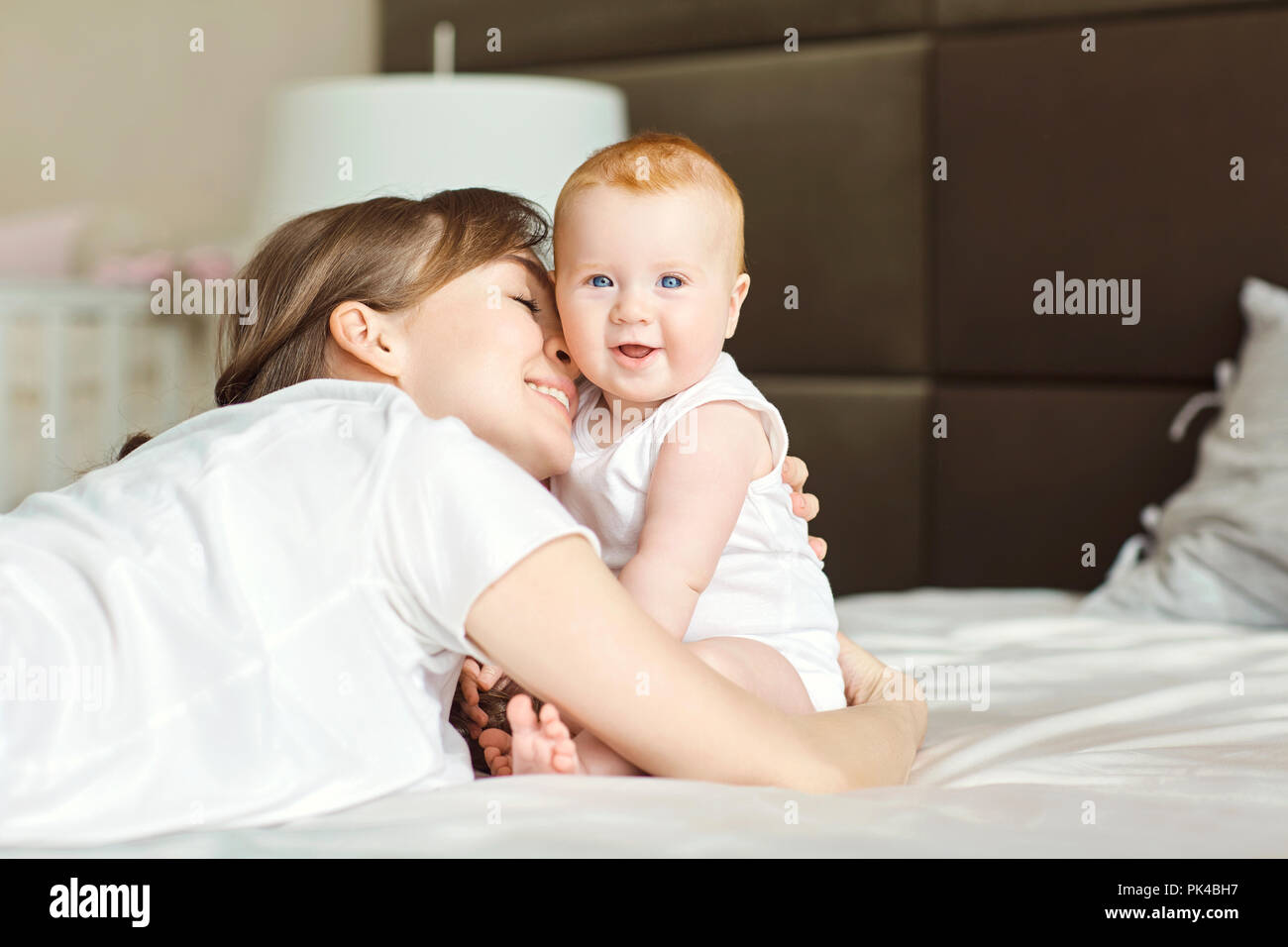 Happy mother hugging baby lying on the bed indoors Stock Photo - Alamy