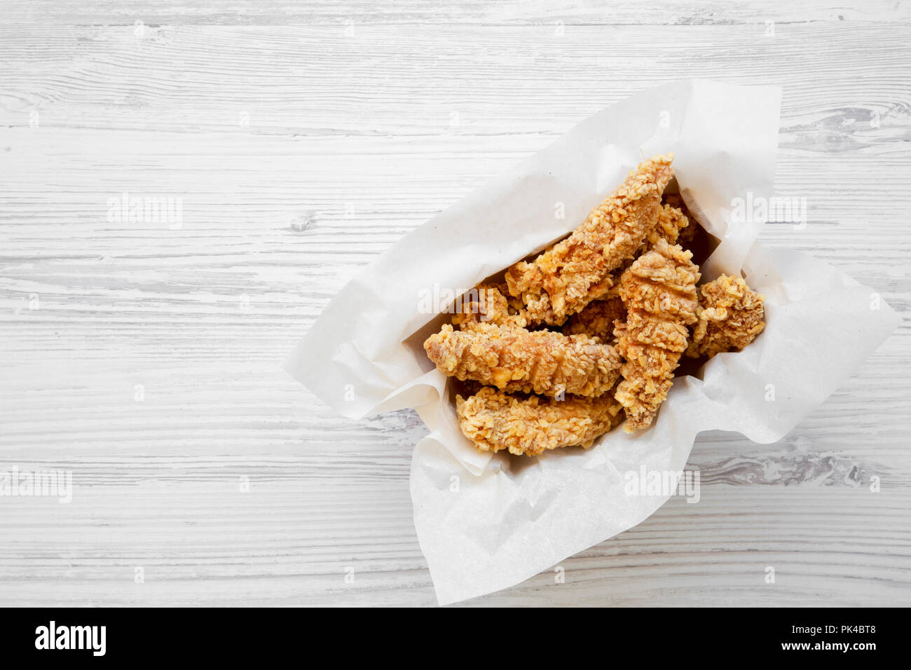 Chicken fingers in paper box on a white wooden table, top view. Flat ...