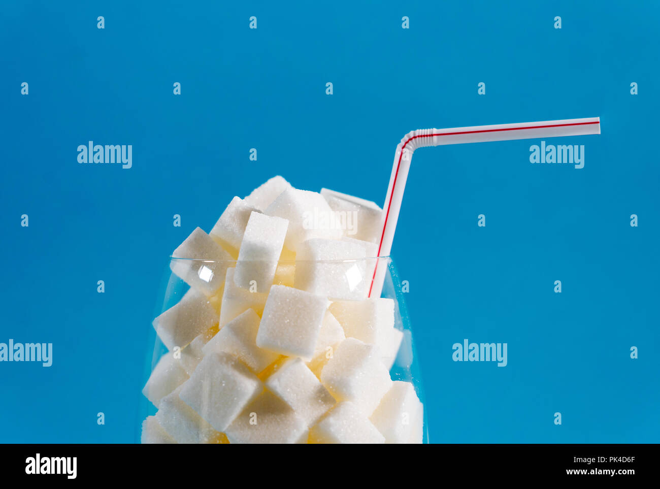 Glass with red stripes straw filled with sugar cubes on blue background ...