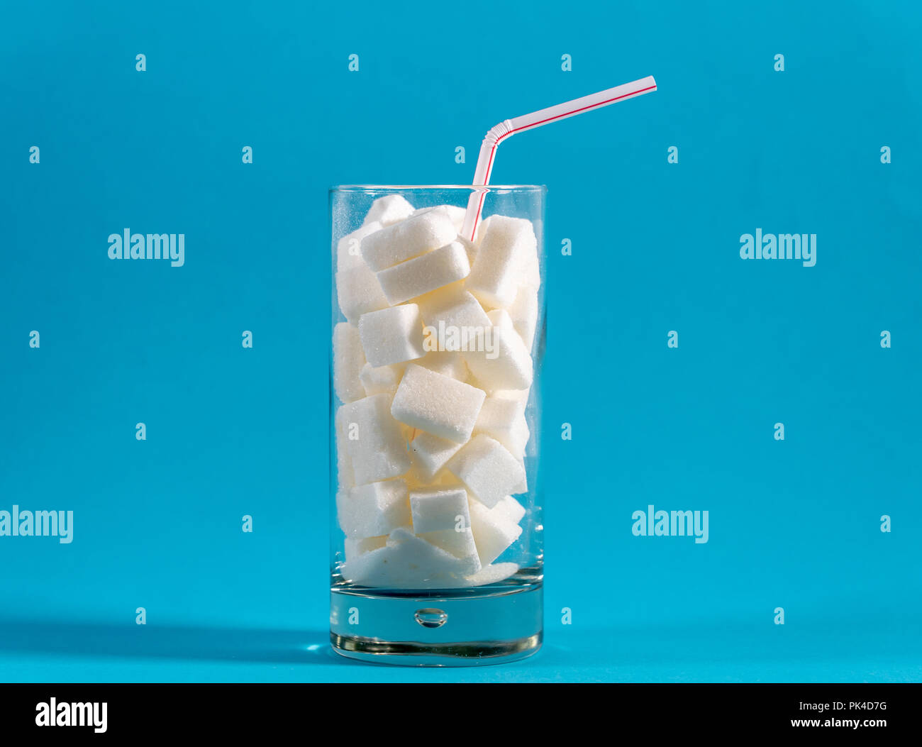 Glass with red stripes straw filled with sugar cubes on blue background ...