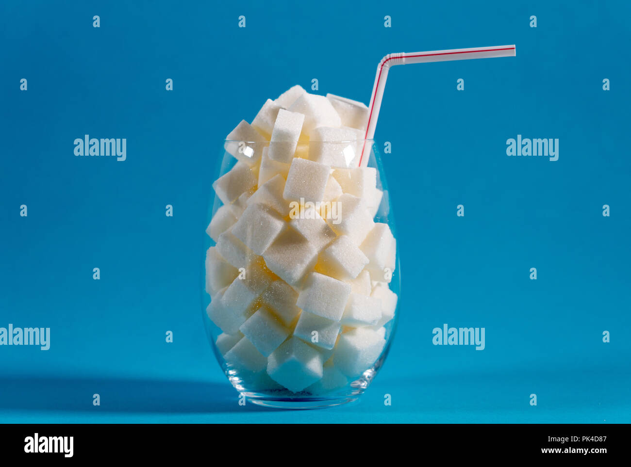 Glass with red stripes straw filled with sugar cubes on blue background ...