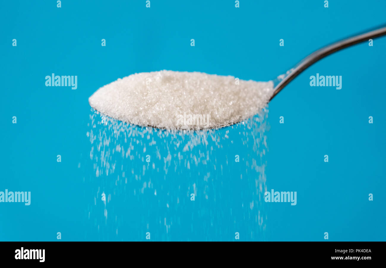 Studio picture of a metal spoon pouring sugar isolated on a blue ...