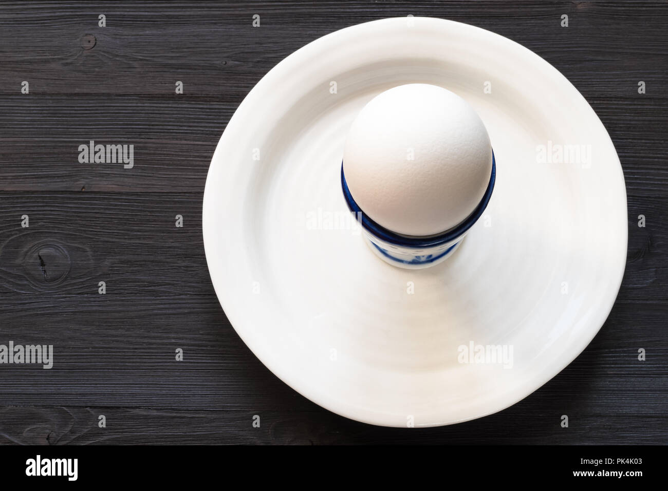 above view of white egg in cup on plate on dark wooden table with blank ...