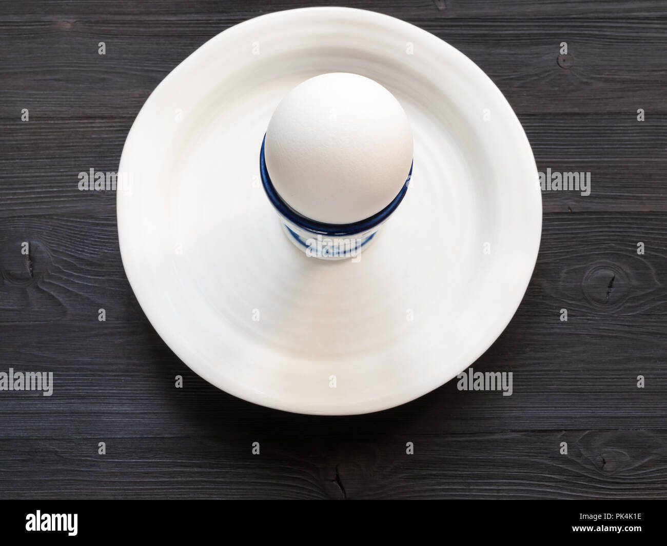 above view of white egg in cup on white plate on dark wooden table ...