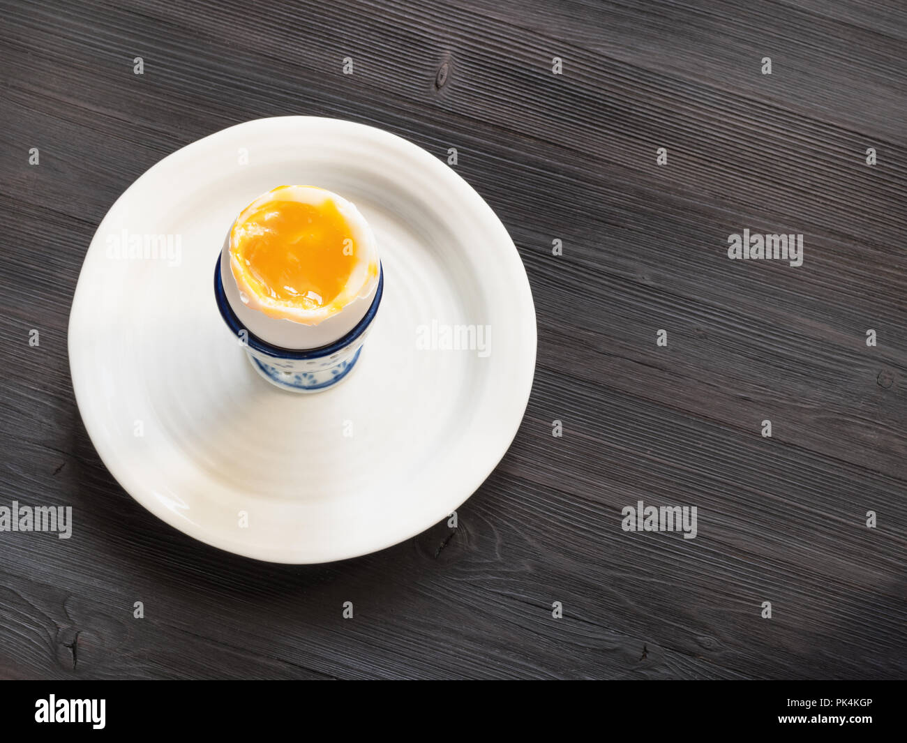 above view of open soft-boiled white egg in cup on plate on dark wooden ...