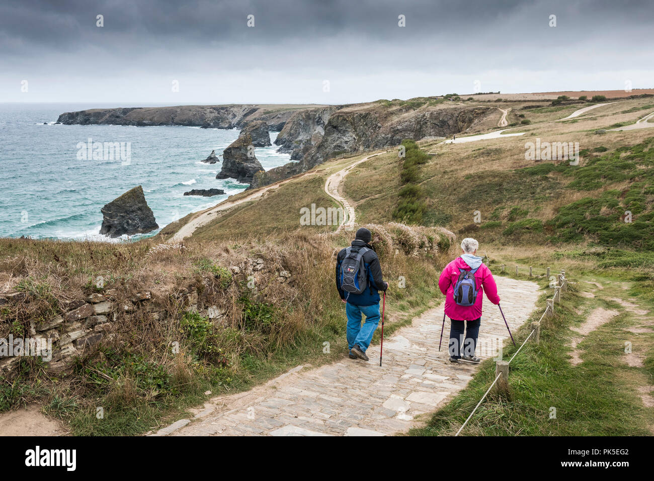 Two mature walkers walking down the South West Coast Path to Bedruthan ...