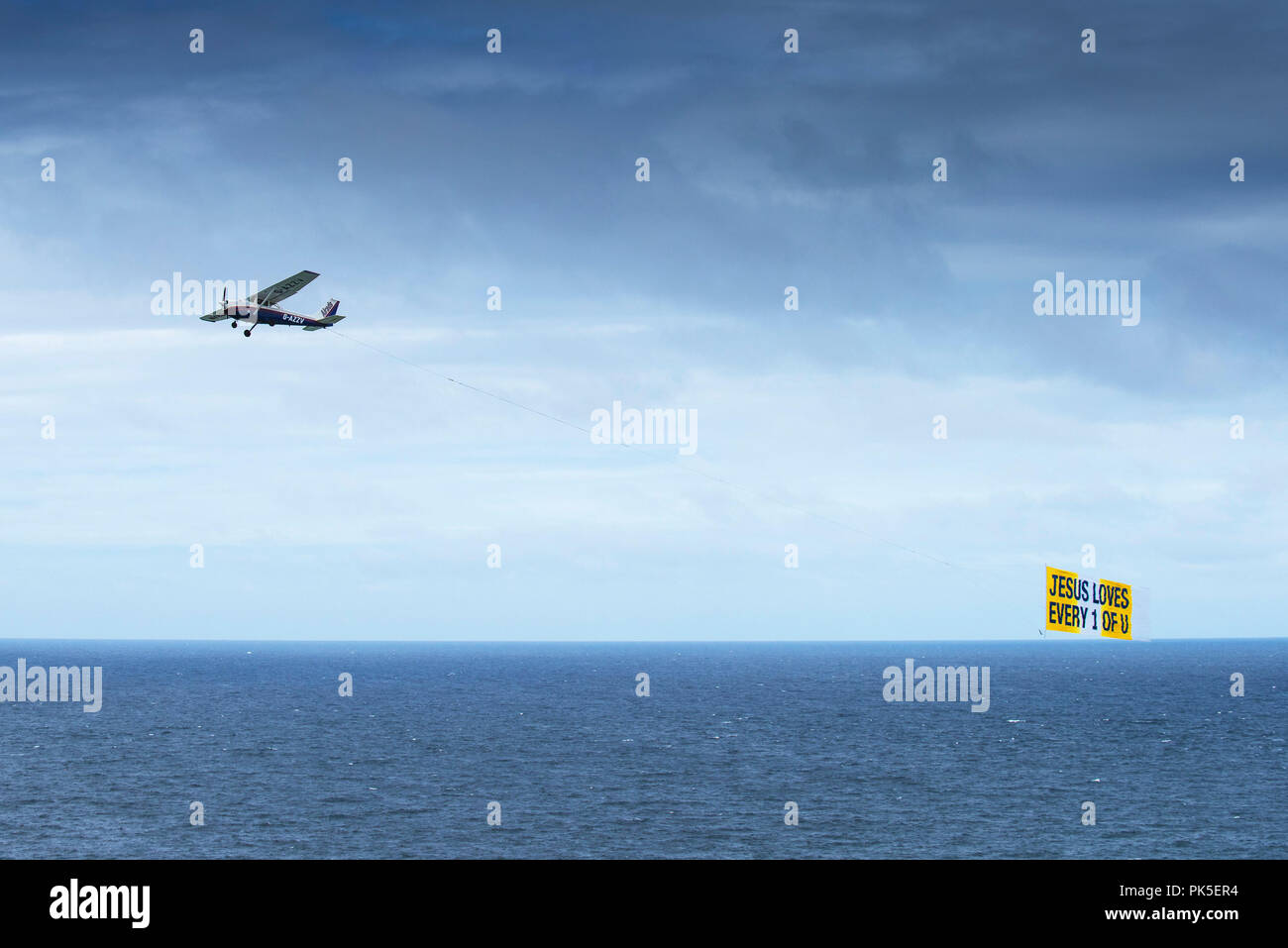 A small aeroplane flying over the sea and towing a banner with a ...