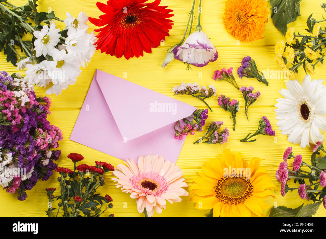 Collection of different flowers and post mail. Yellow wooden desk ...