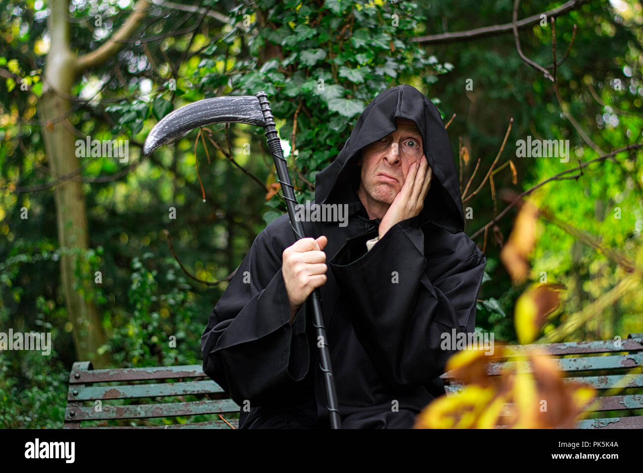 The Grimm Reaper sits on a park bench looking unhappy Stock Photo - Alamy