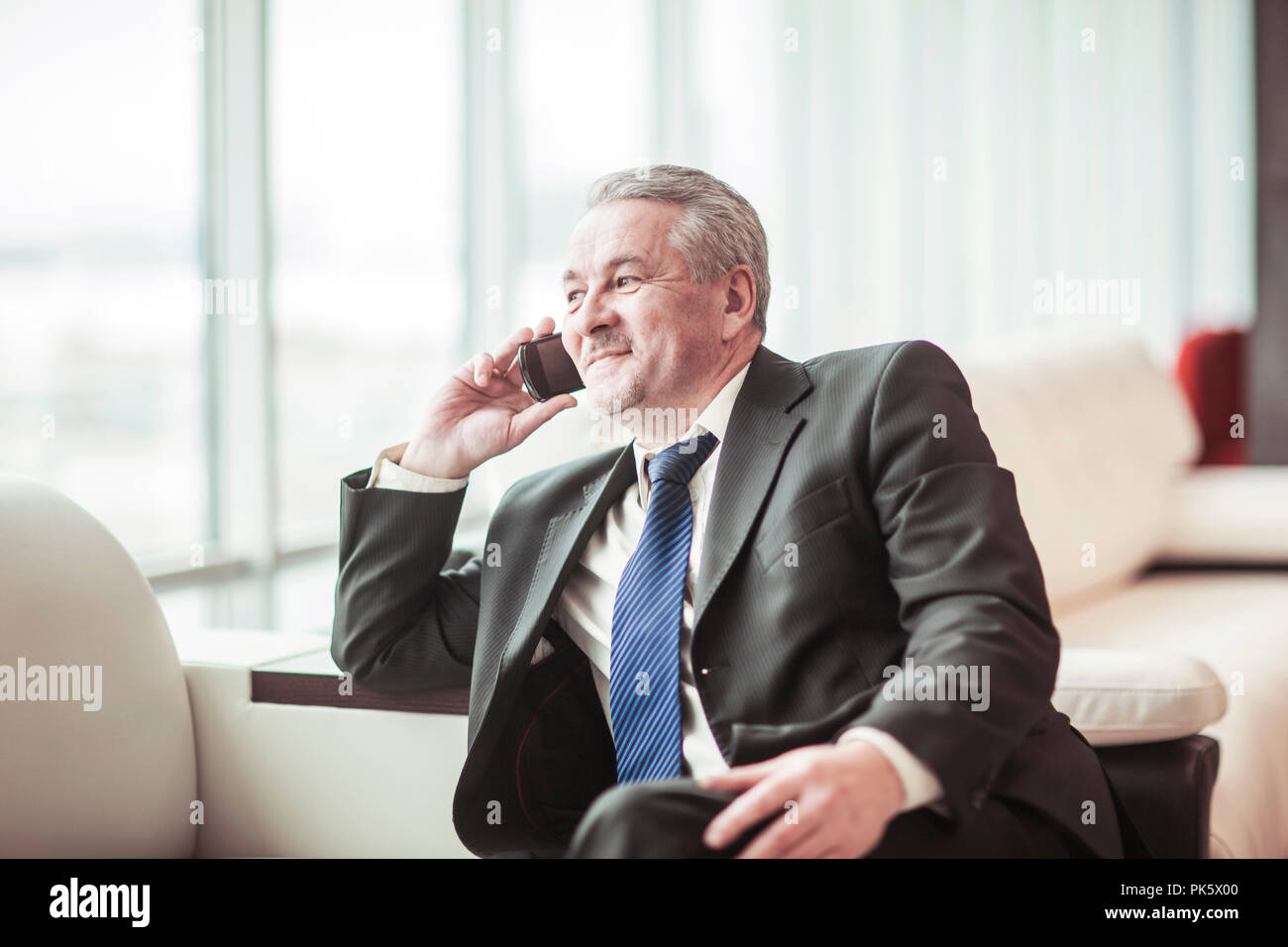successful businessman talking on his smartphone sitting on couch in ...