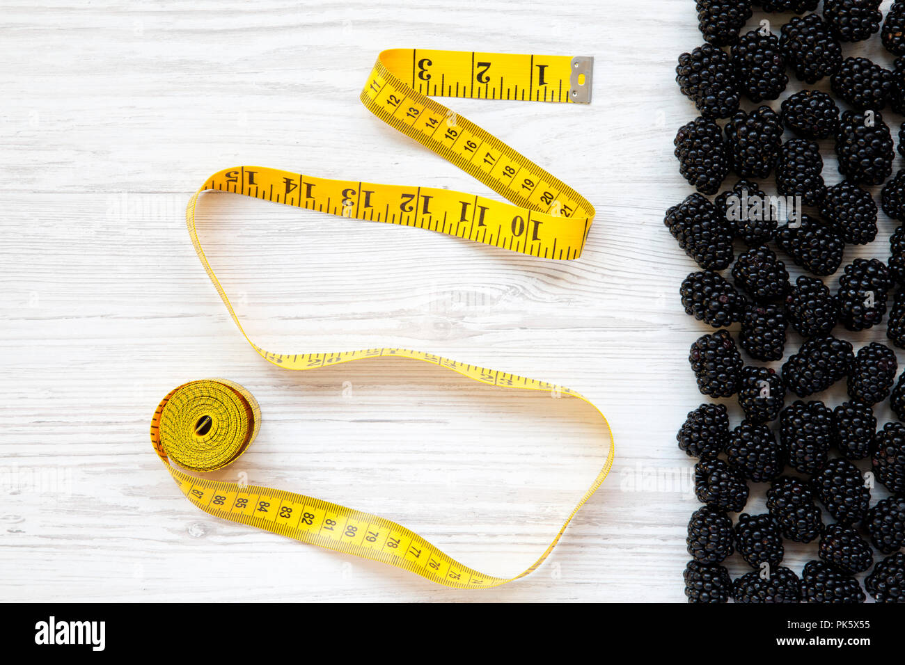 Blackberries and yellow measuring tape on white wooden table, top view ...