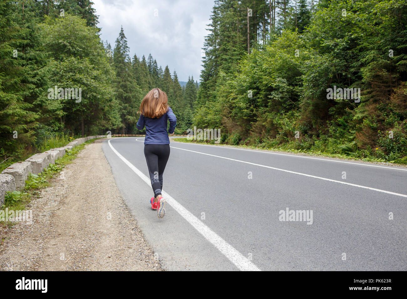 Running girl on the road. Young slim woman jogging in mountains. Rear ...