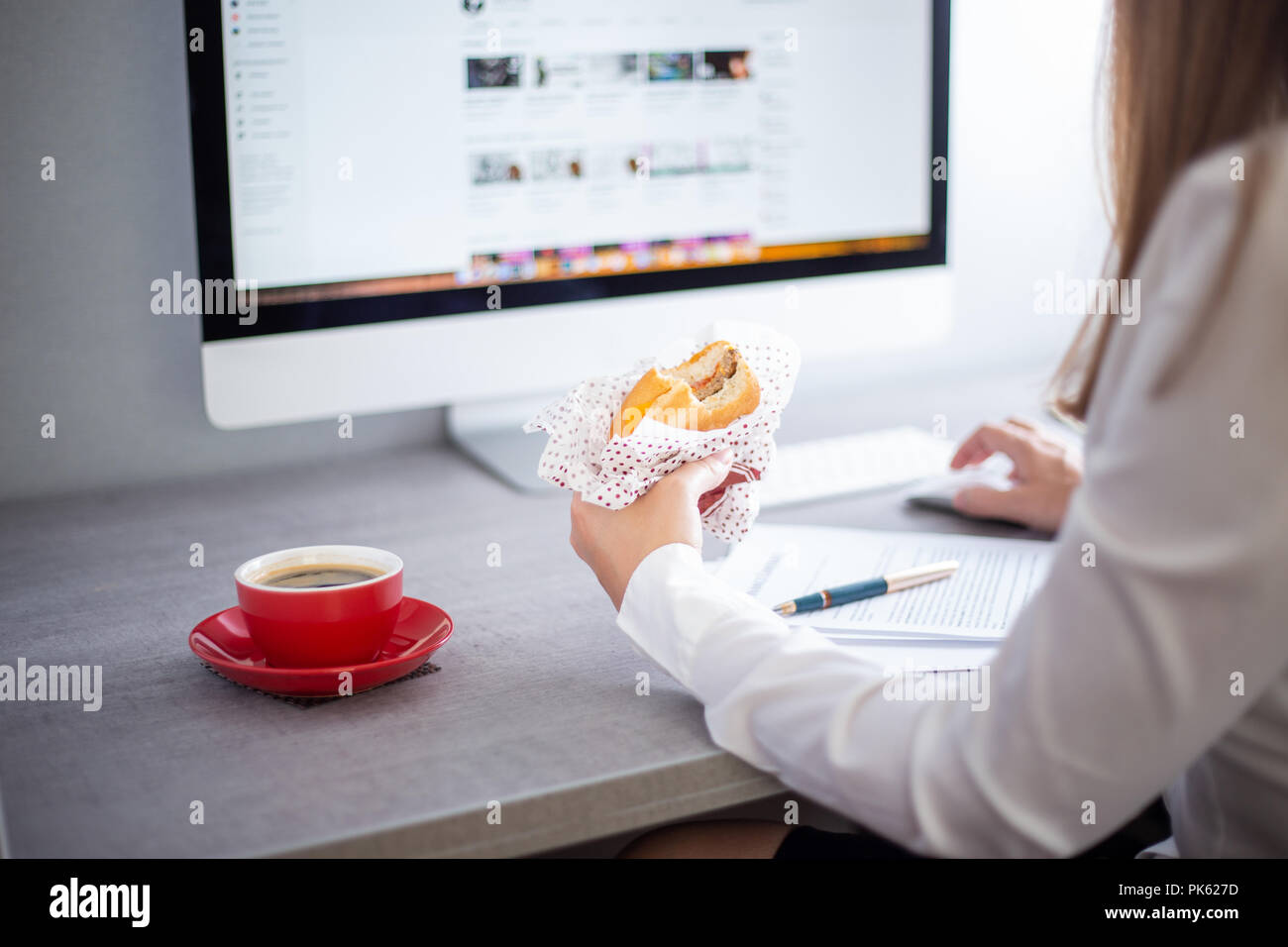 Young business woman eating burger at the desk Stock Photo - Alamy