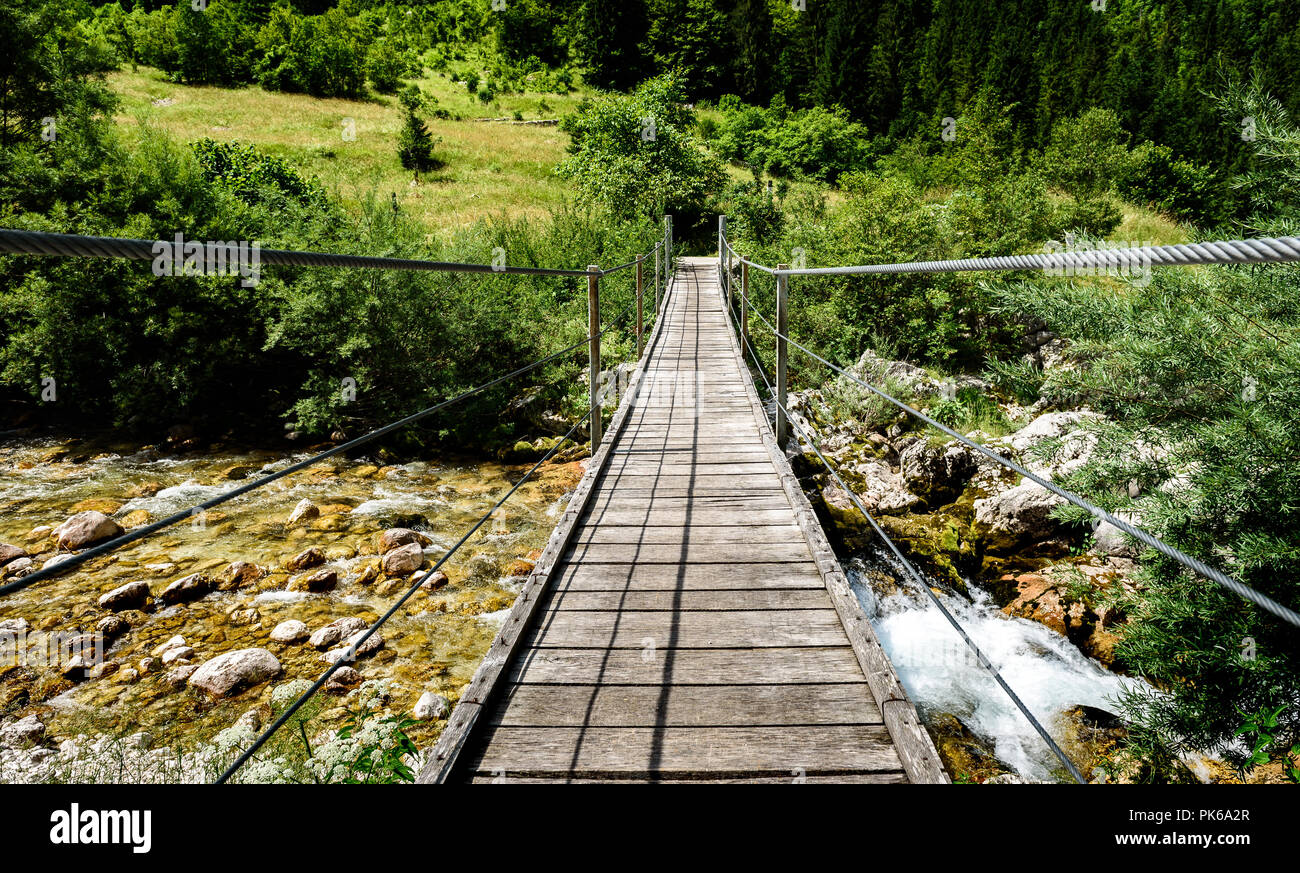Wooden hanging bridge leading forward over green mountain river ...