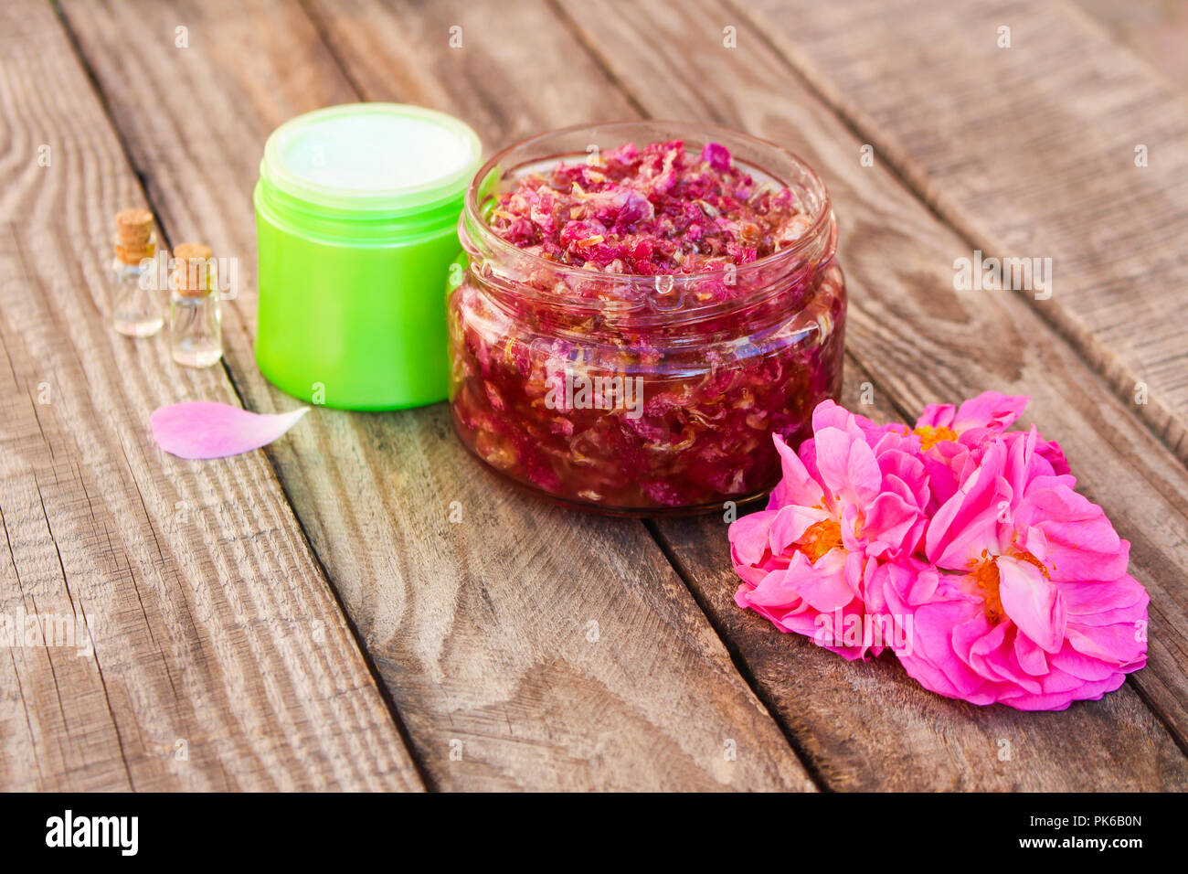 Jam jar, face cream, bottle of essential oil of rose petals on wooden ...