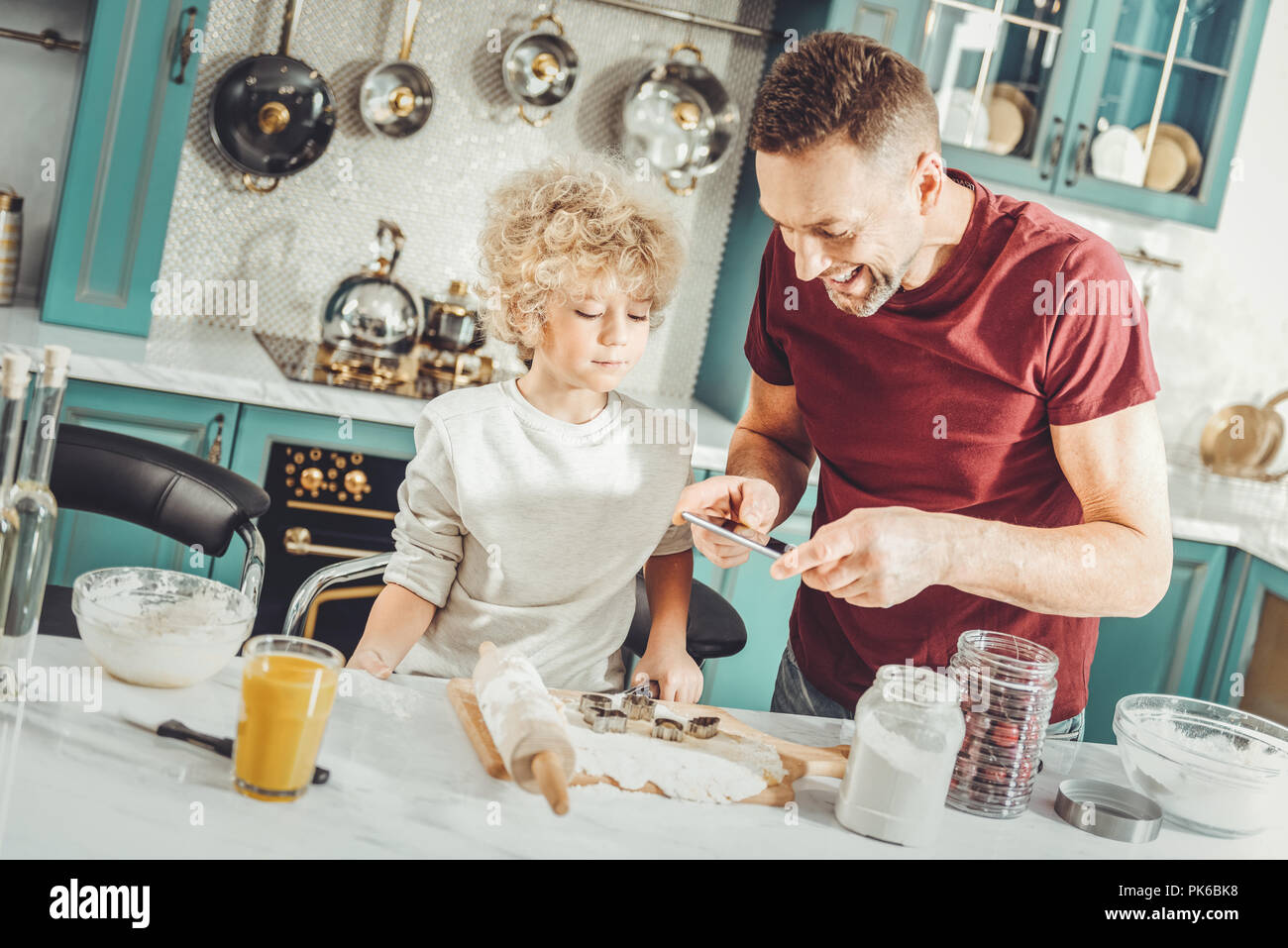 Smiling man making photo of future cookies while cooking with son Stock ...