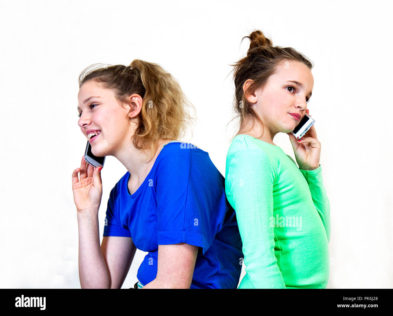 Two pretty preteen girls having fun together. Talking on phones ...