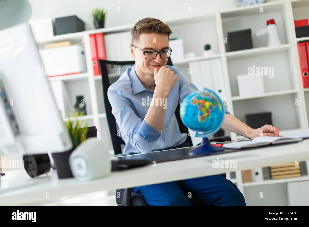 A young man sits in the office at a computer desk and in front of him ...
