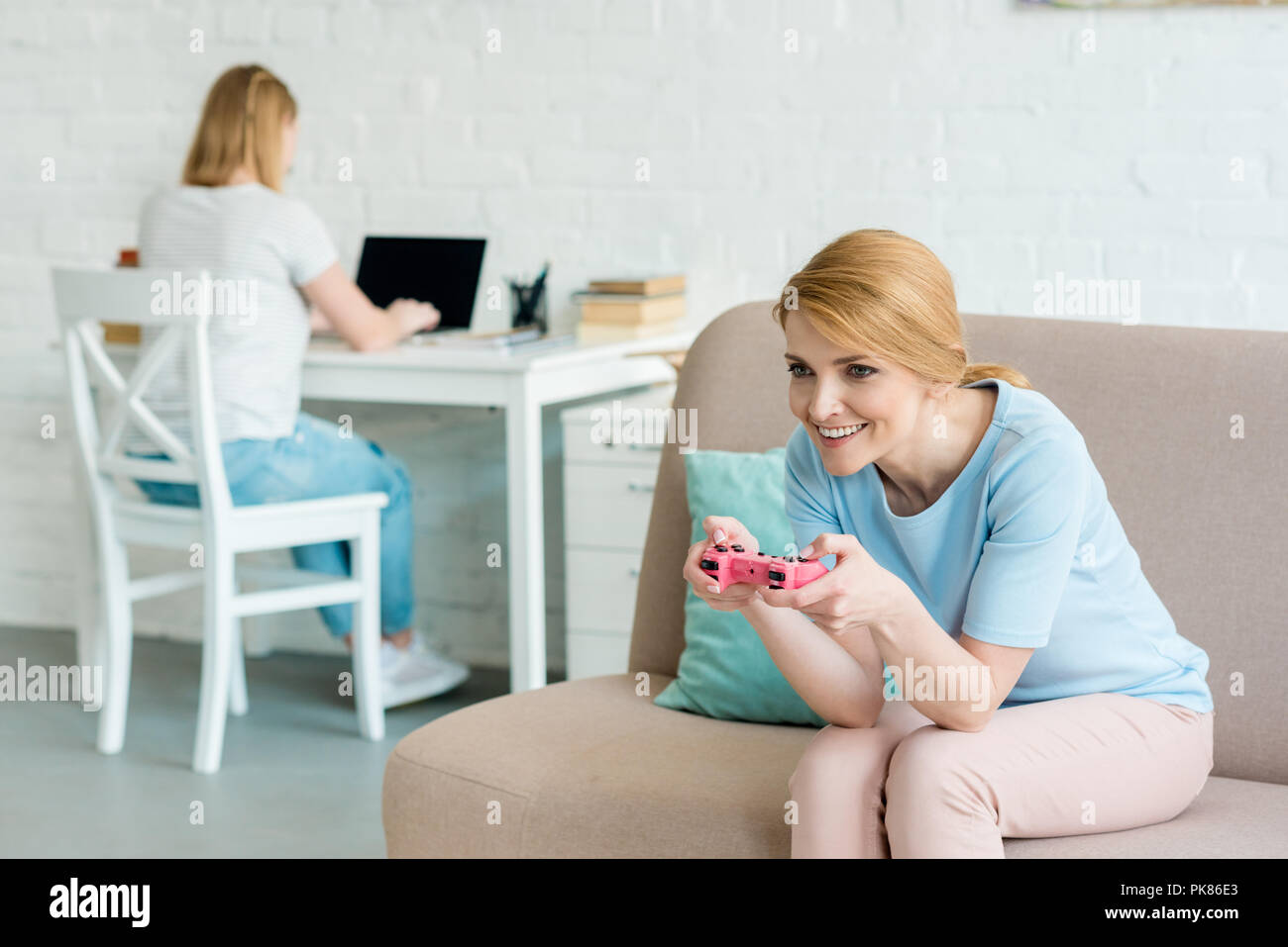 mother playing console game while her daughter working with laptop ...