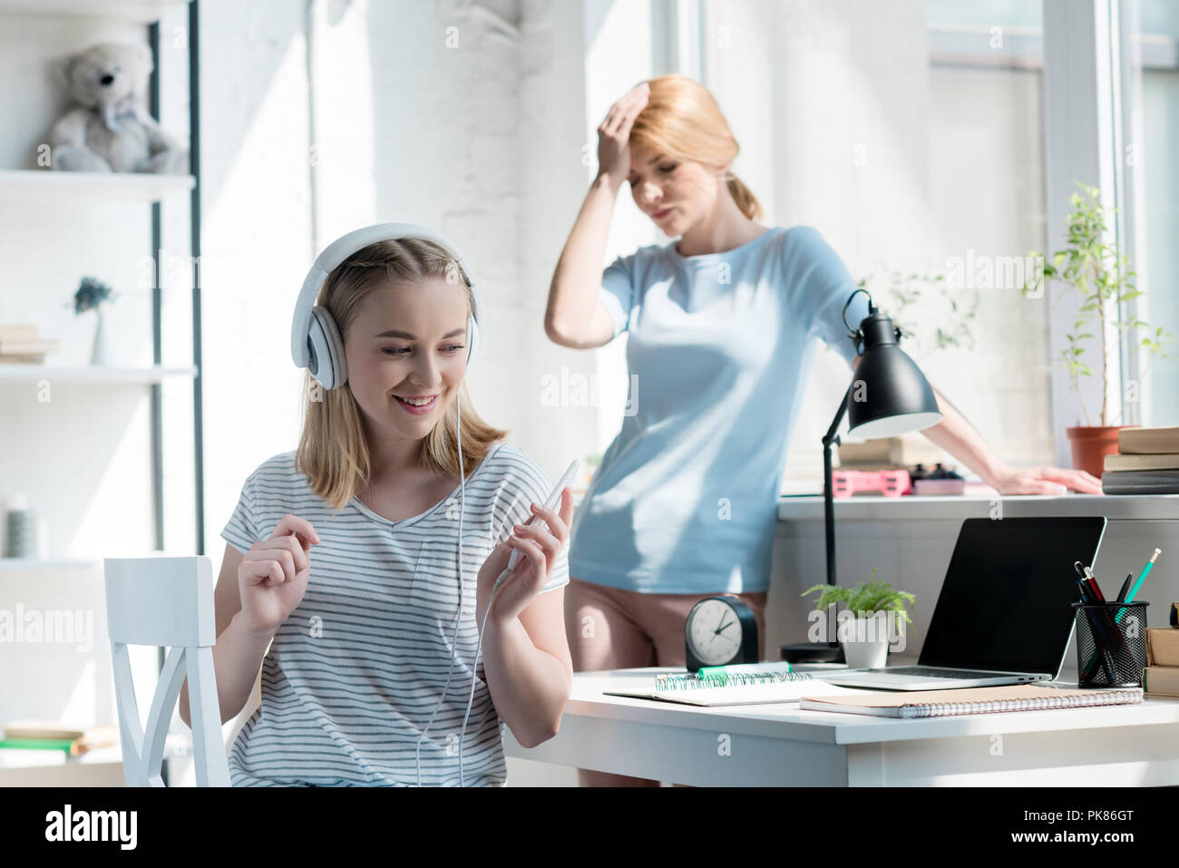happy teen daughter listening music while her disappointed mother ...