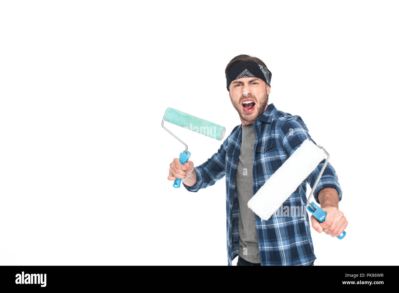 angry young man in headband holding paint rollers isolated on white ...