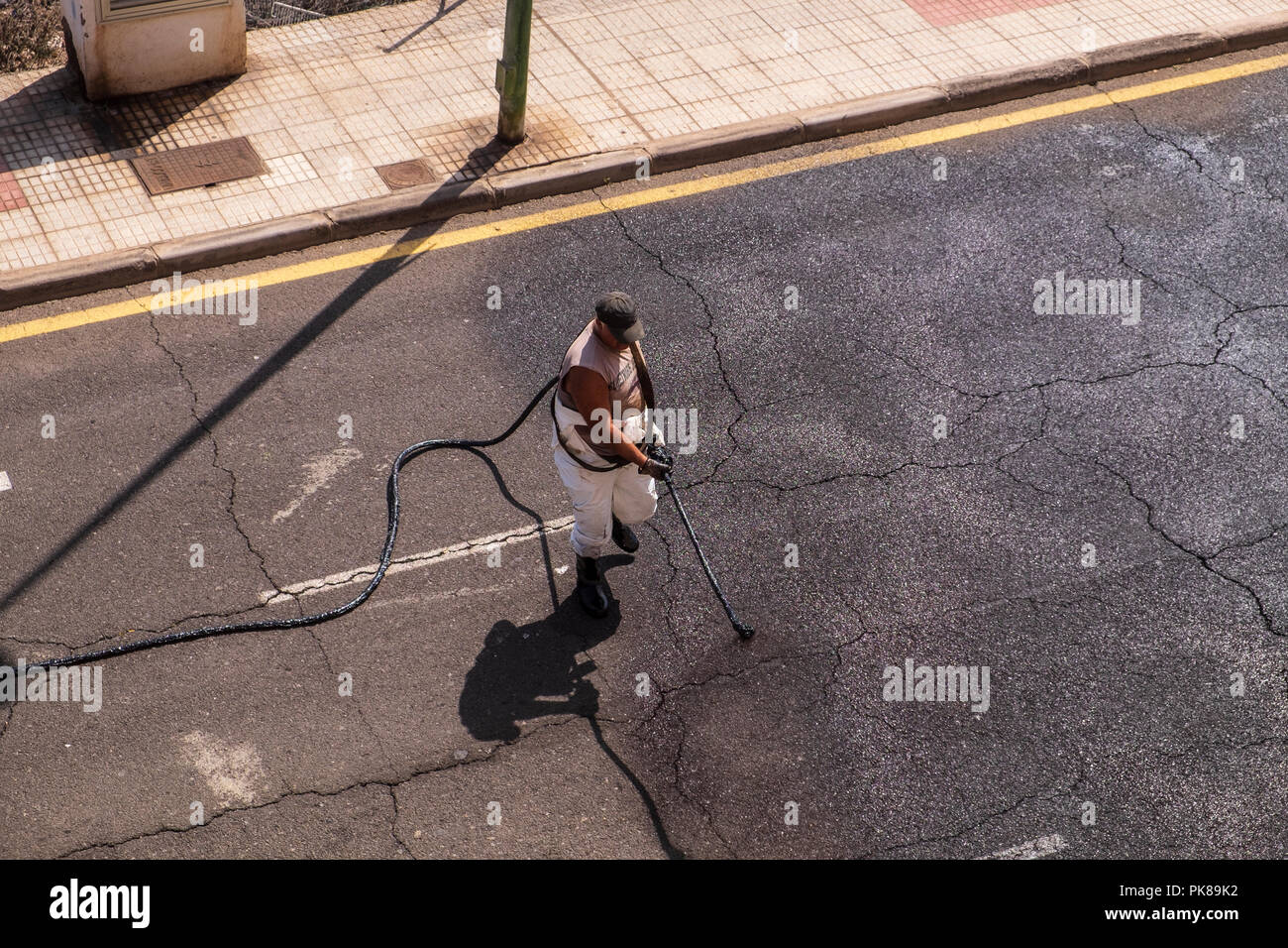 Workman spraying tar on to a road in preparation for a new layer of ...