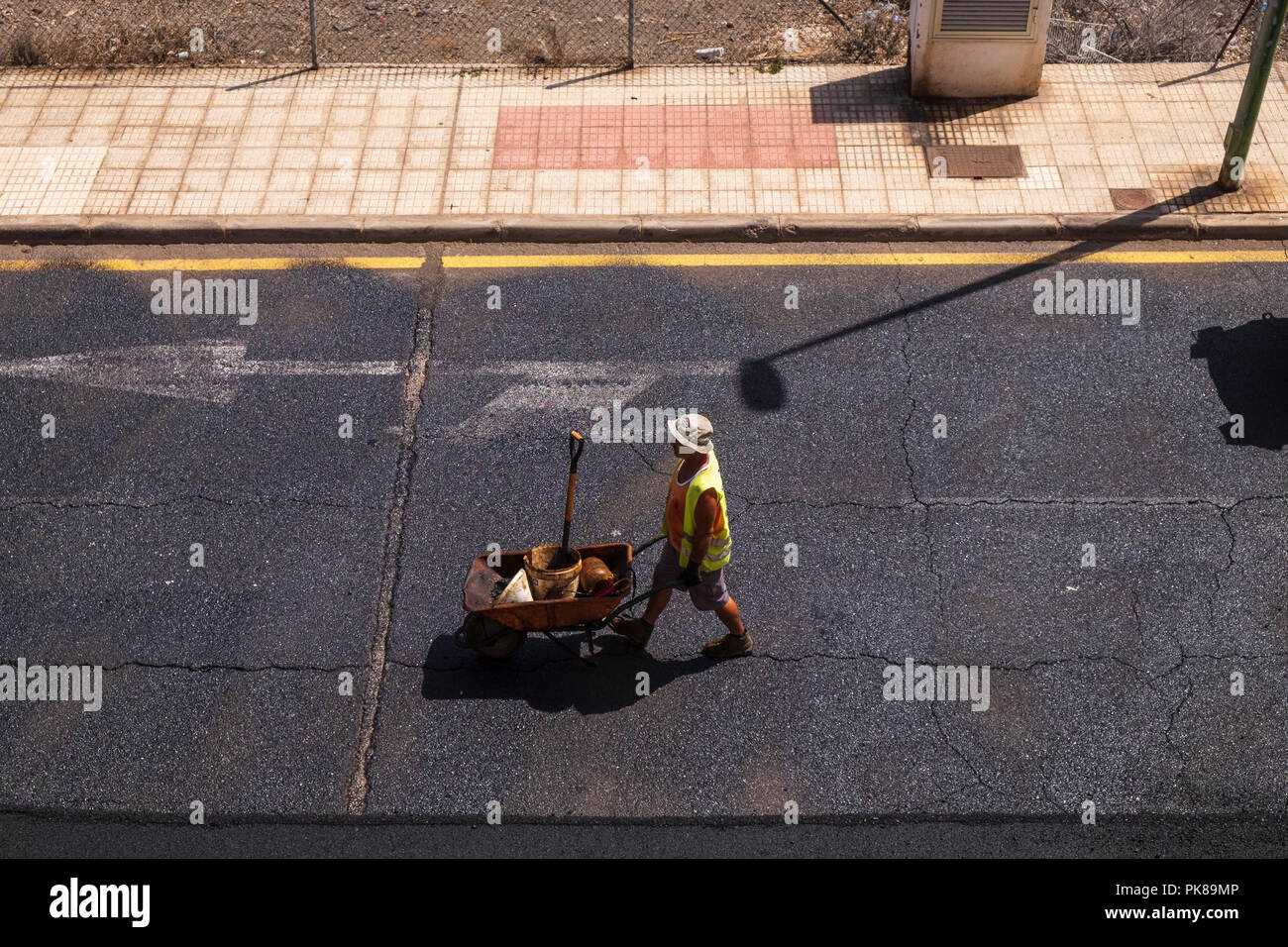 Workman with wheelbarrow during laying a new layer of asphalt on a road ...