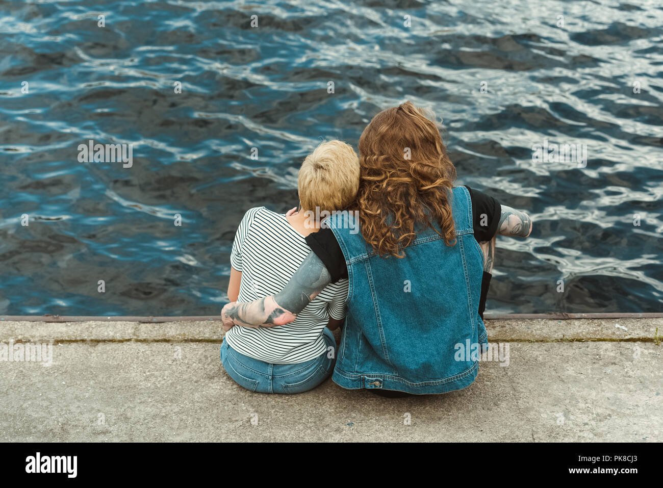 rear view of couple hugging and sitting on bridge near river Stock ...
