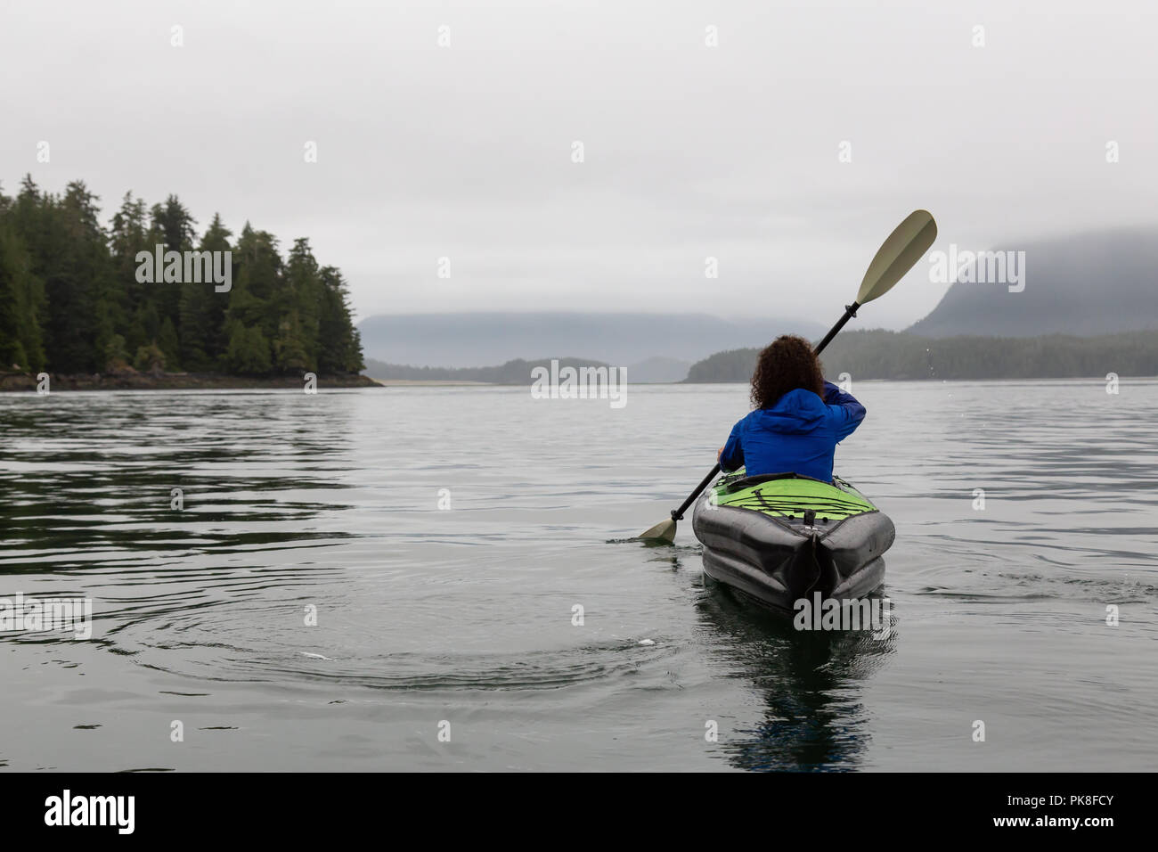 Girl kayaking in the ocean during a cloudy and gloomy sunrise. Taken in ...