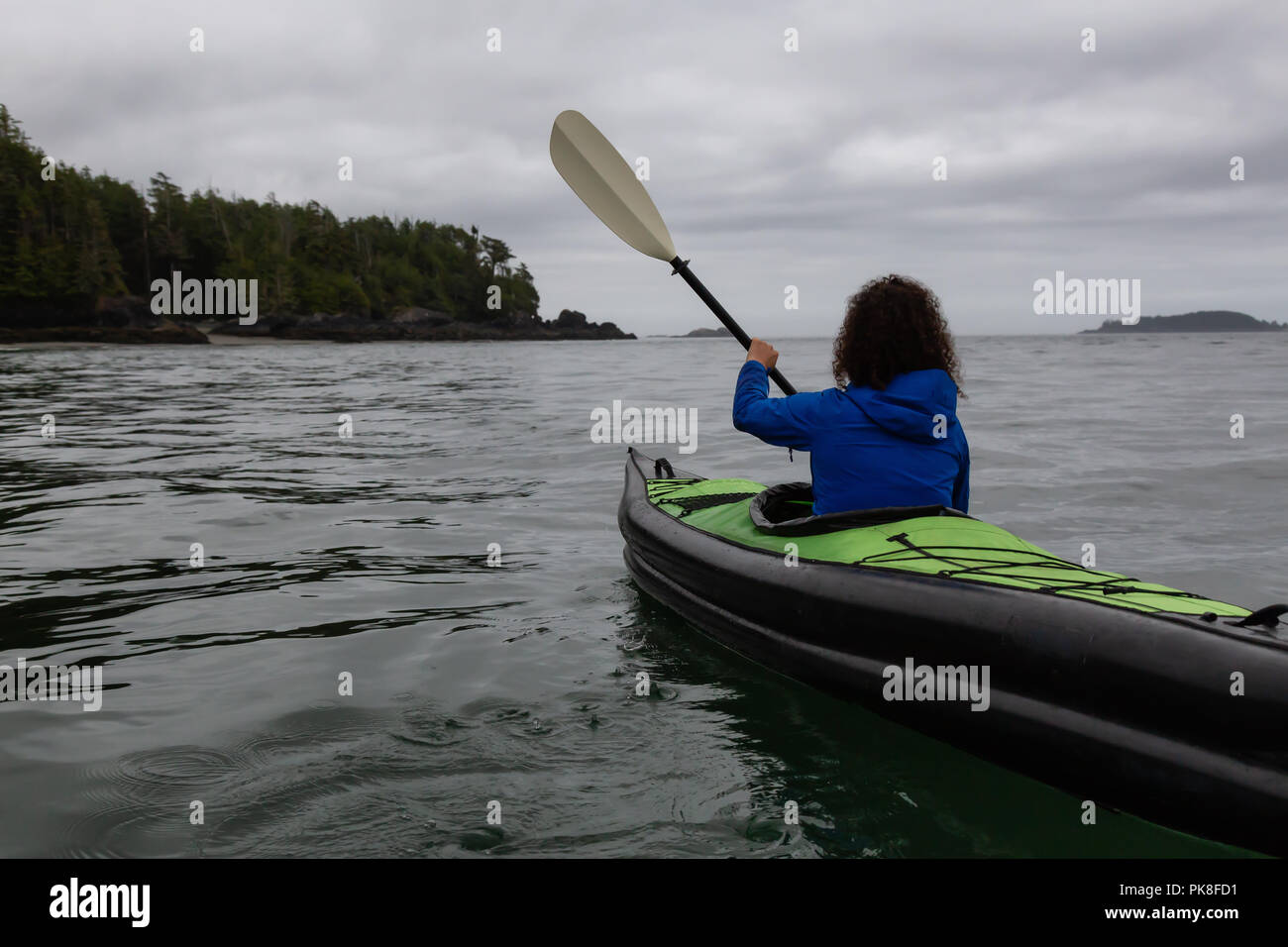 Girl kayaking in the ocean during a cloudy and gloomy sunrise. Taken in ...