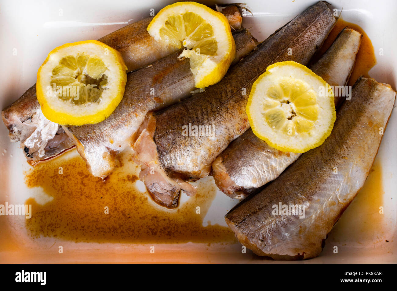 Raw fish hake with lemon slices, spices, olive oil on white pan Stock ...