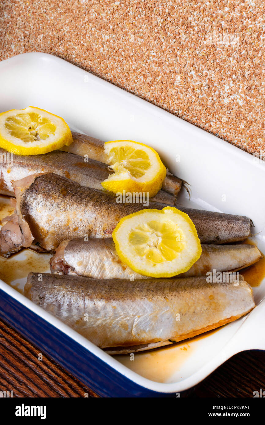 Raw fish hake with lemon slices, spices, olive oil on white pan Stock ...