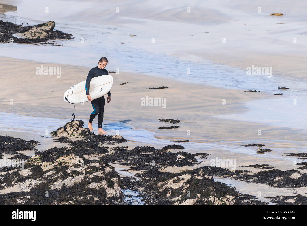 A tired surfer carrying his surfboard walking across Little Fistralm ...