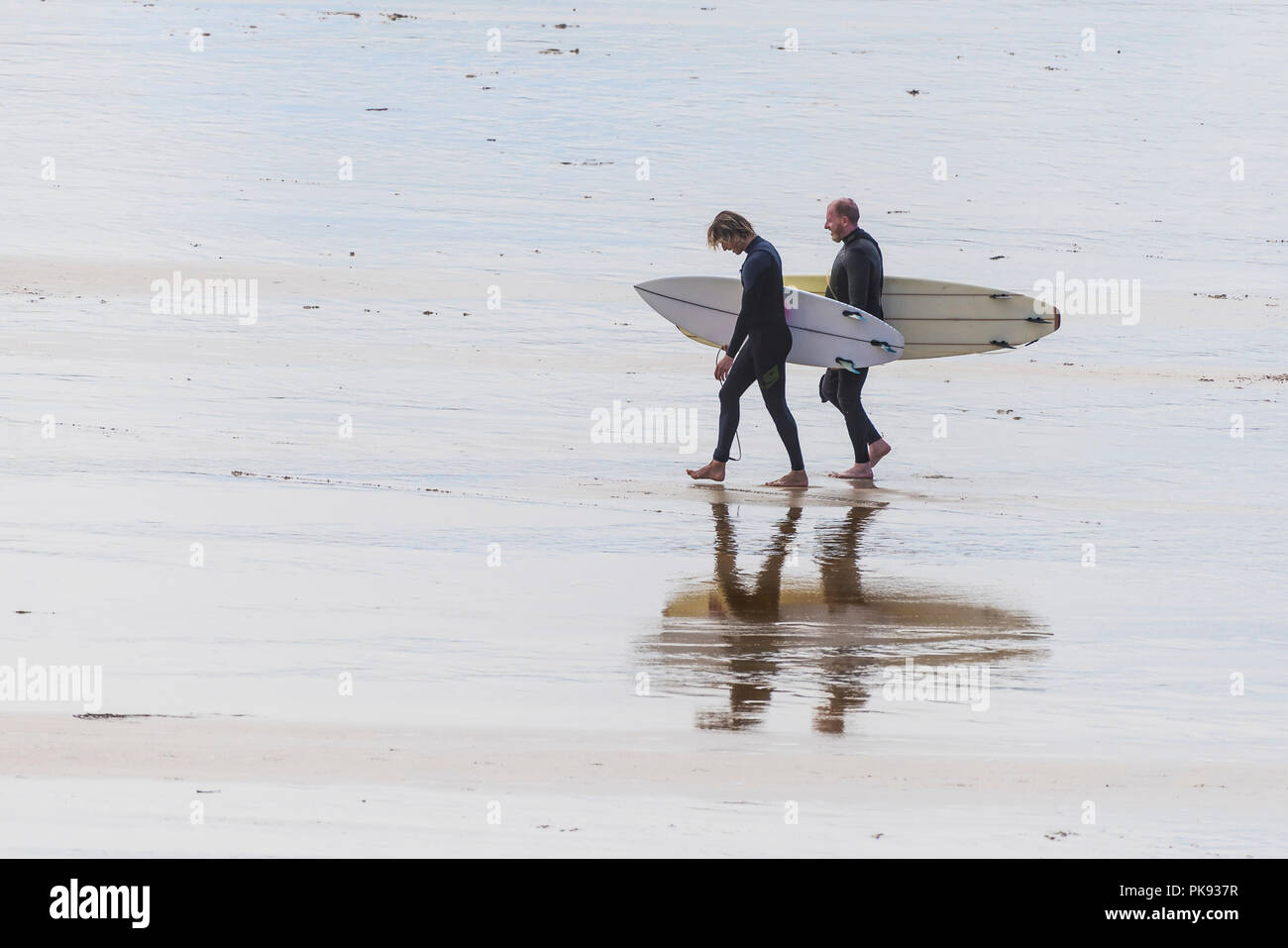 Tired surfers walking across Fistral Beach after as surfing session ...