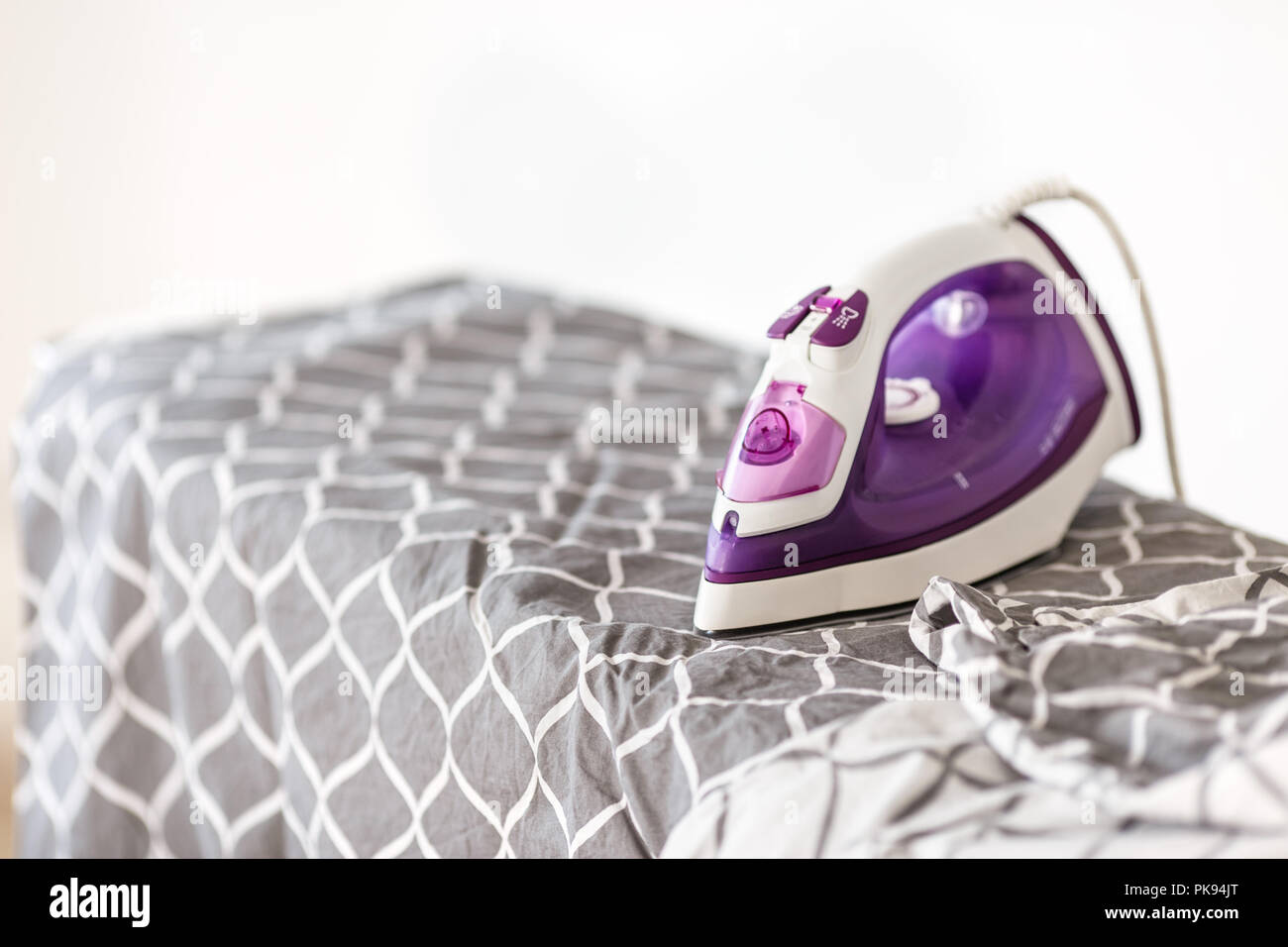 Iron on ironing board on light home interior background. Ironing bed ...