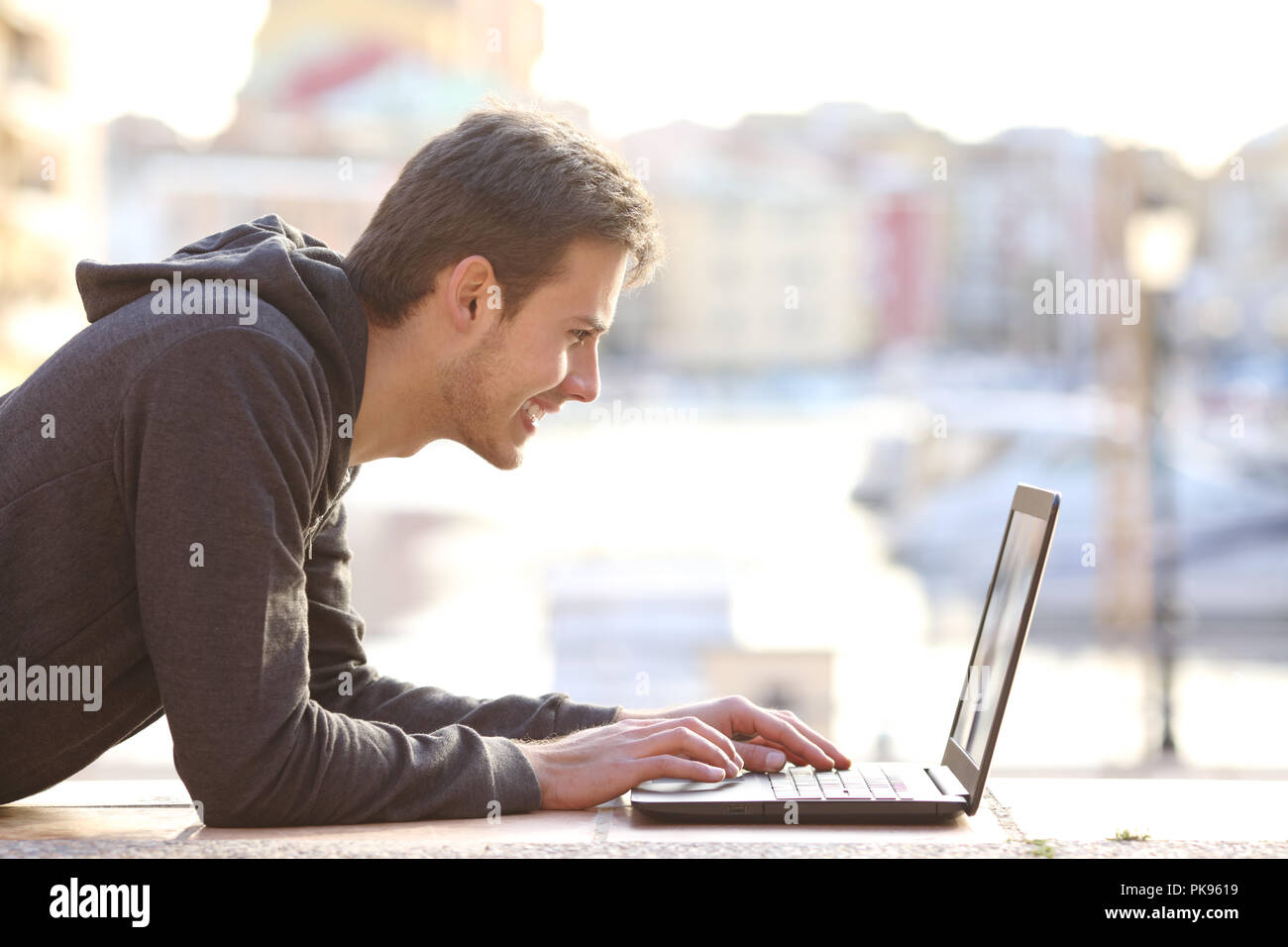 Side view portrait of a happy teenage boy writing in a laptop on ...