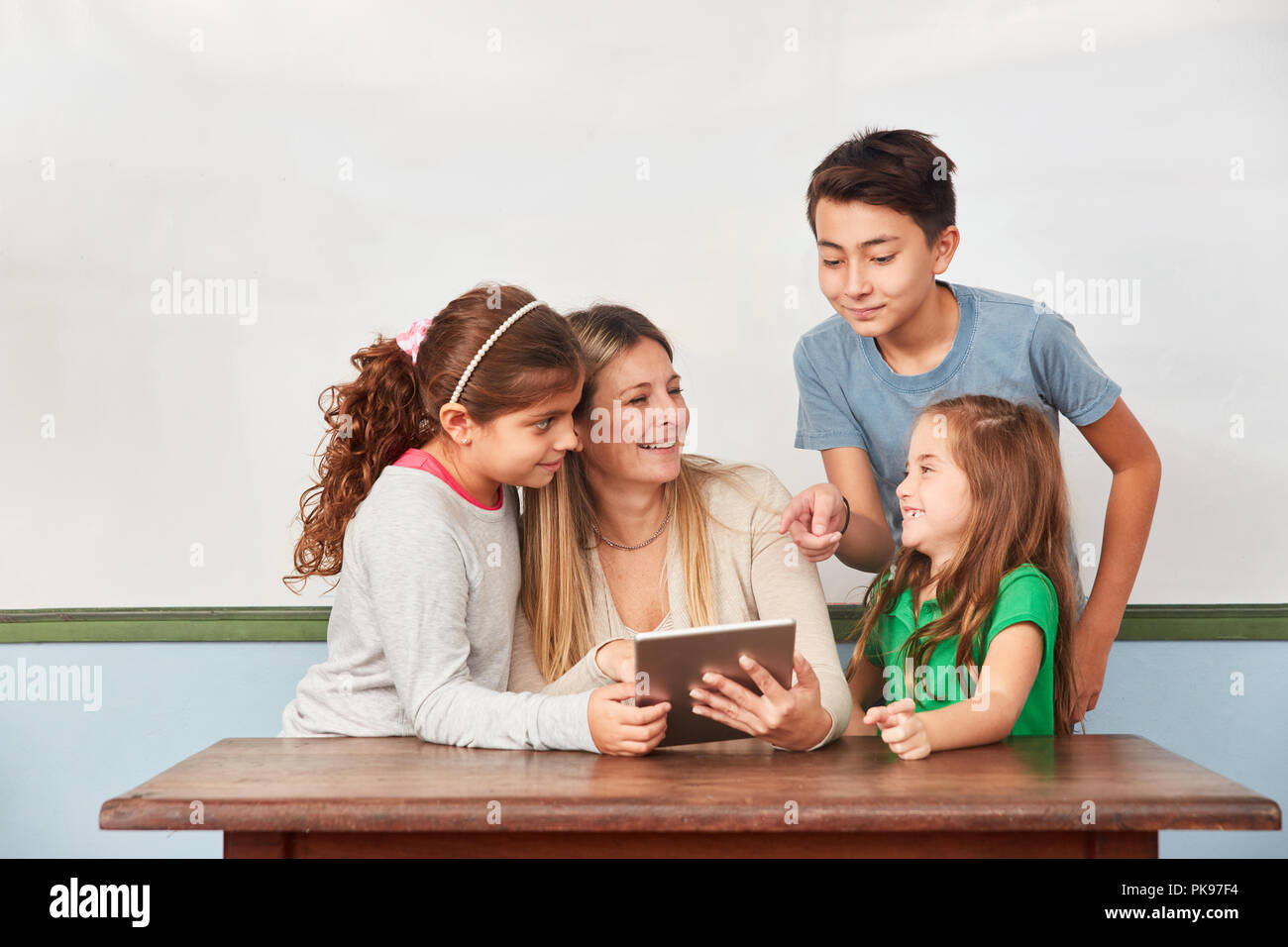 Children And Teacher Working Together On Tablet Computer In Computer Science Lessons Stock Photo children-and-teacher-working-together-on-tablet-computer-in-computer-science-lessons-stock-photo