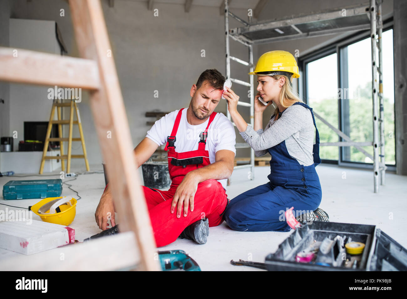 A woman with smartphone helping man worker after an accident at the ...