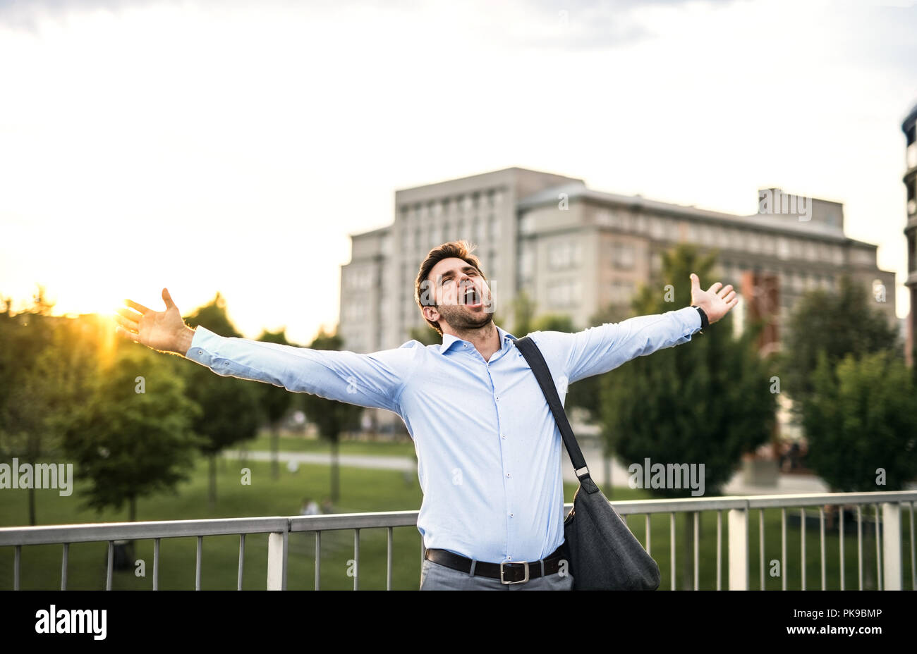 A happy businessman standing on a bridge, screaming and stretching arms ...