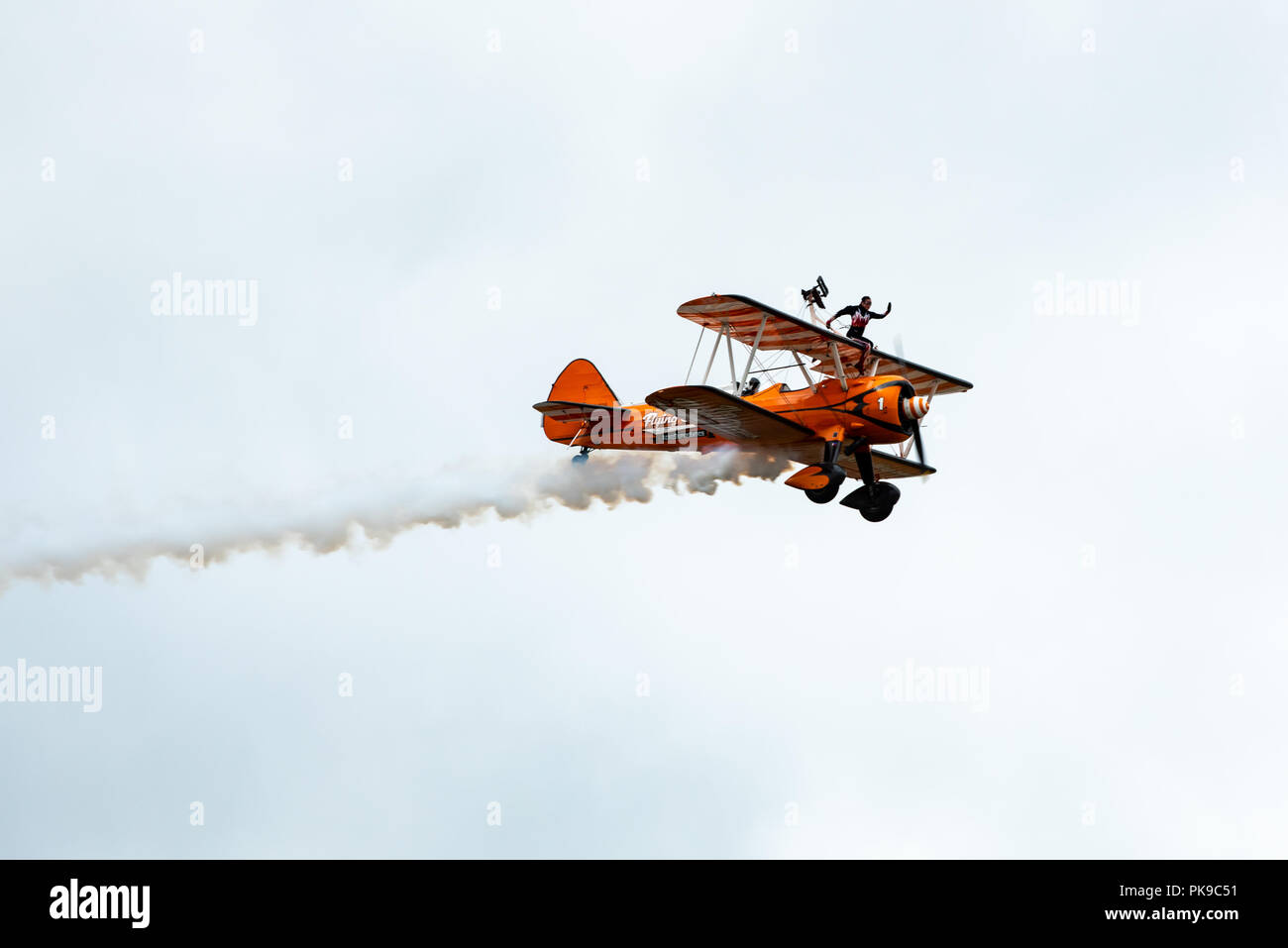 A wing walker sits, unharnessed, on the top wing of an AeroSuperBatics ...