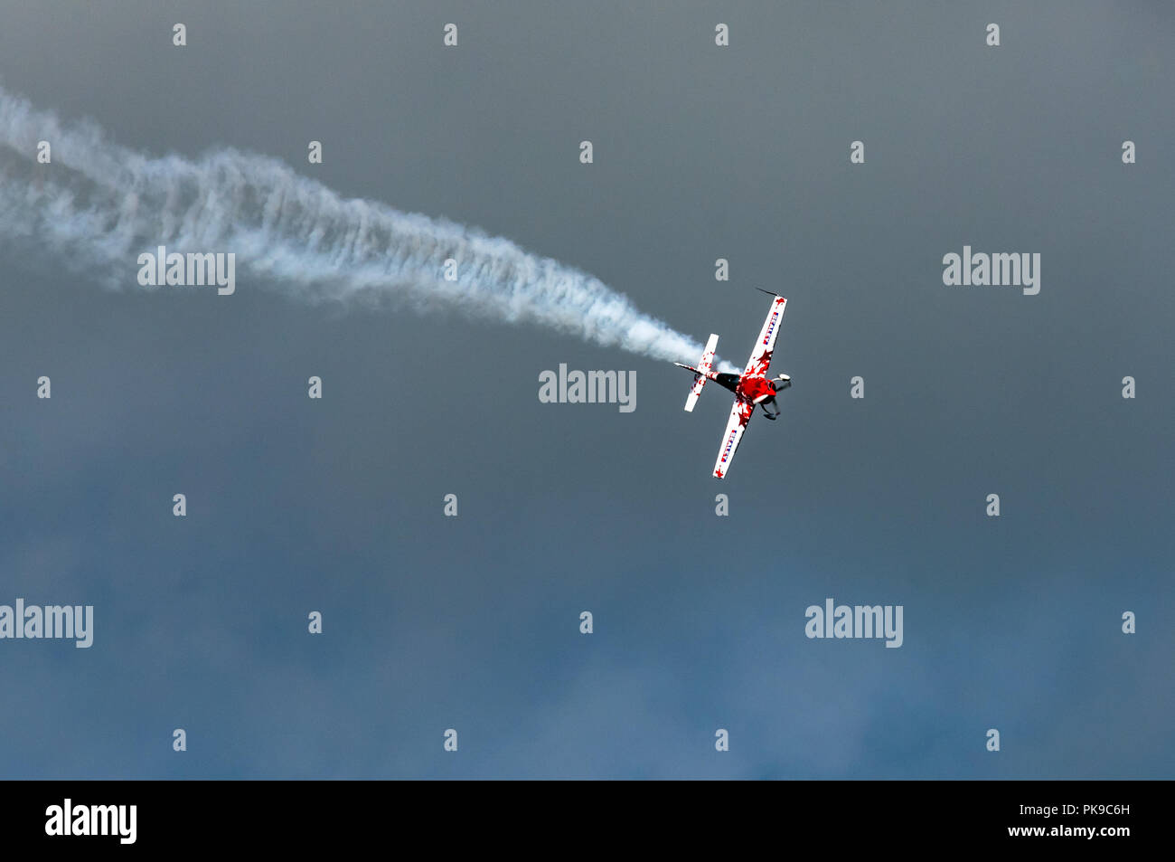 A plume of white smoke trails behind a G-Force Aerobatics Extra 300 ...