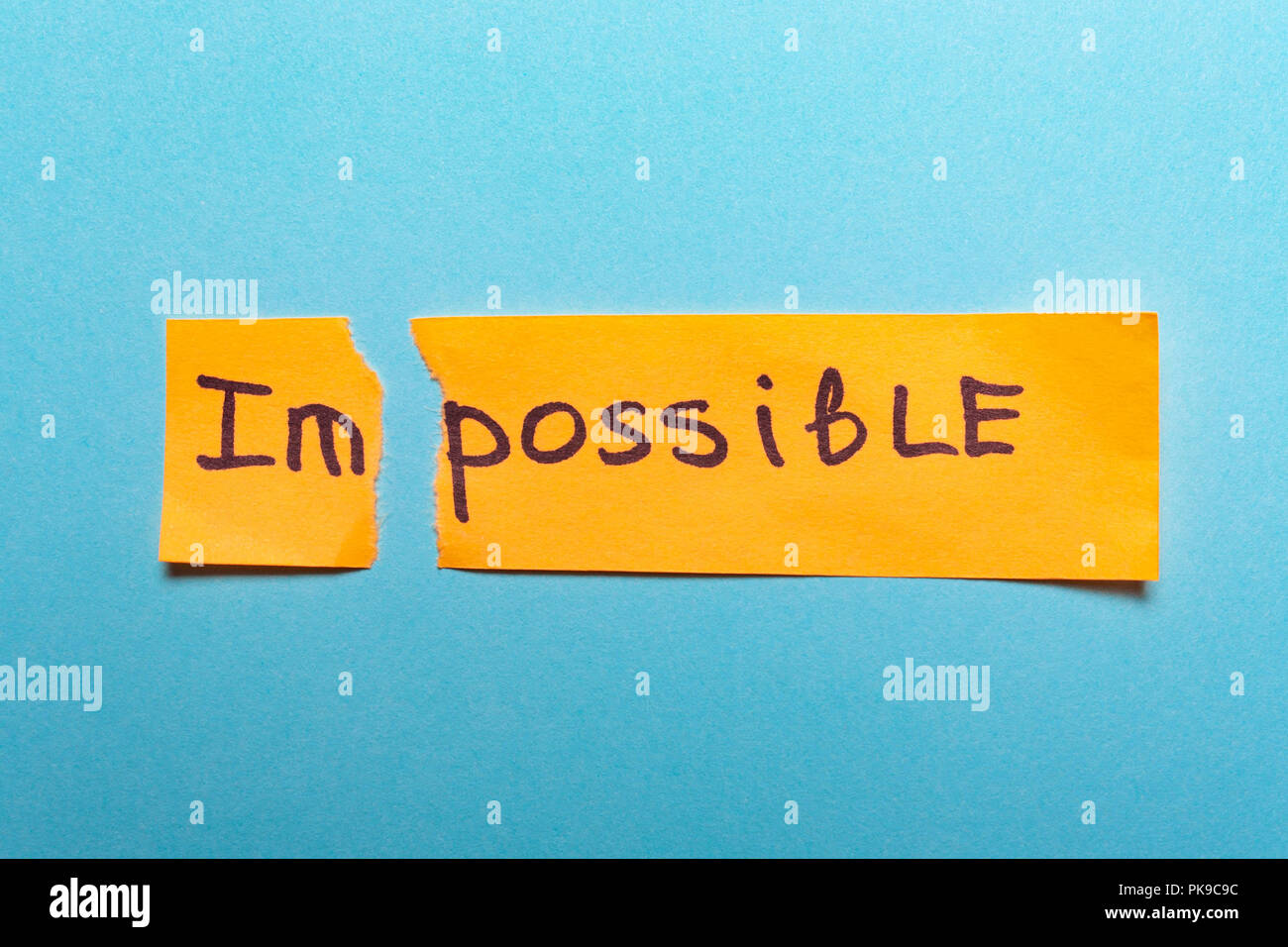 The word impossible is written on yellow paper and torn on a blue ...