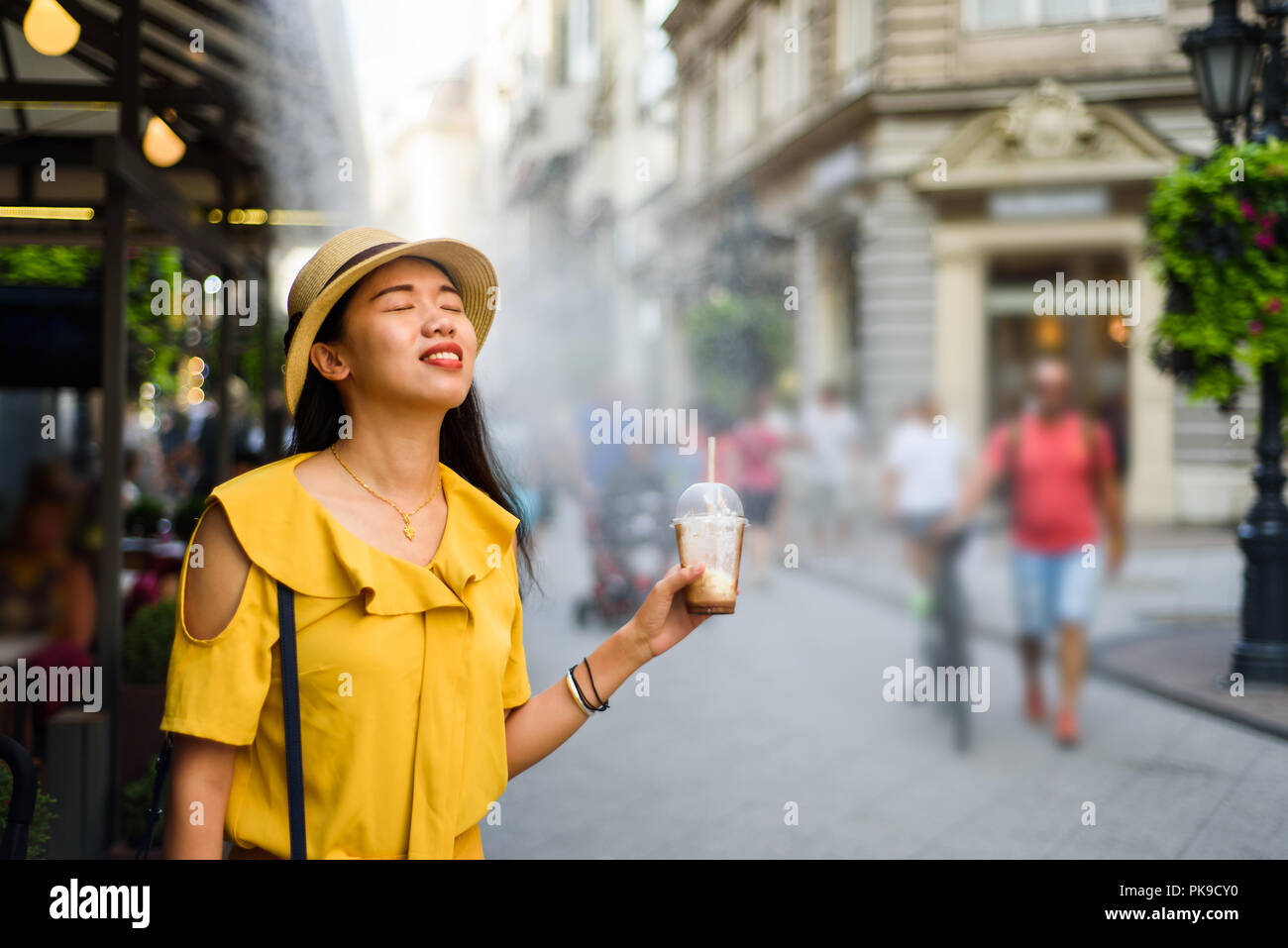 Girl refreshing in a water fan cooling on the street with coffee to go ...