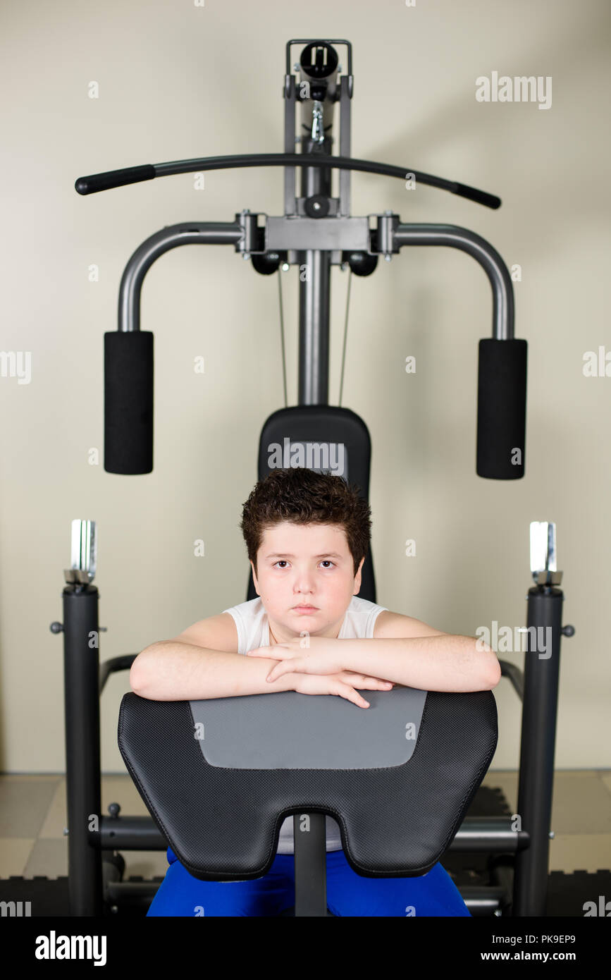 cute fat little caucasian boy sitting on sport exercise machine in ...